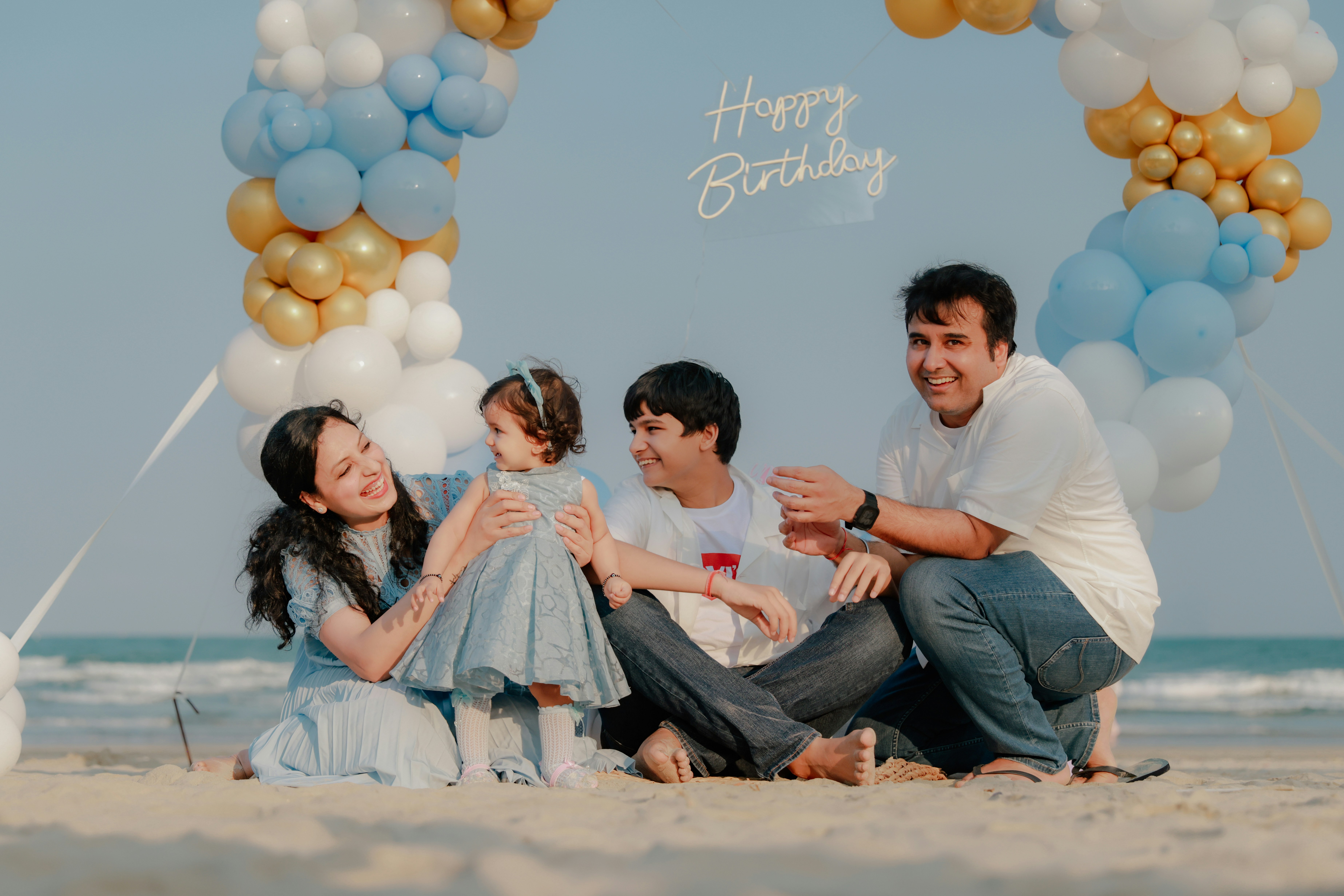 Sunlit Birthday on the Shore: A Family Moment by the Balloon Arch