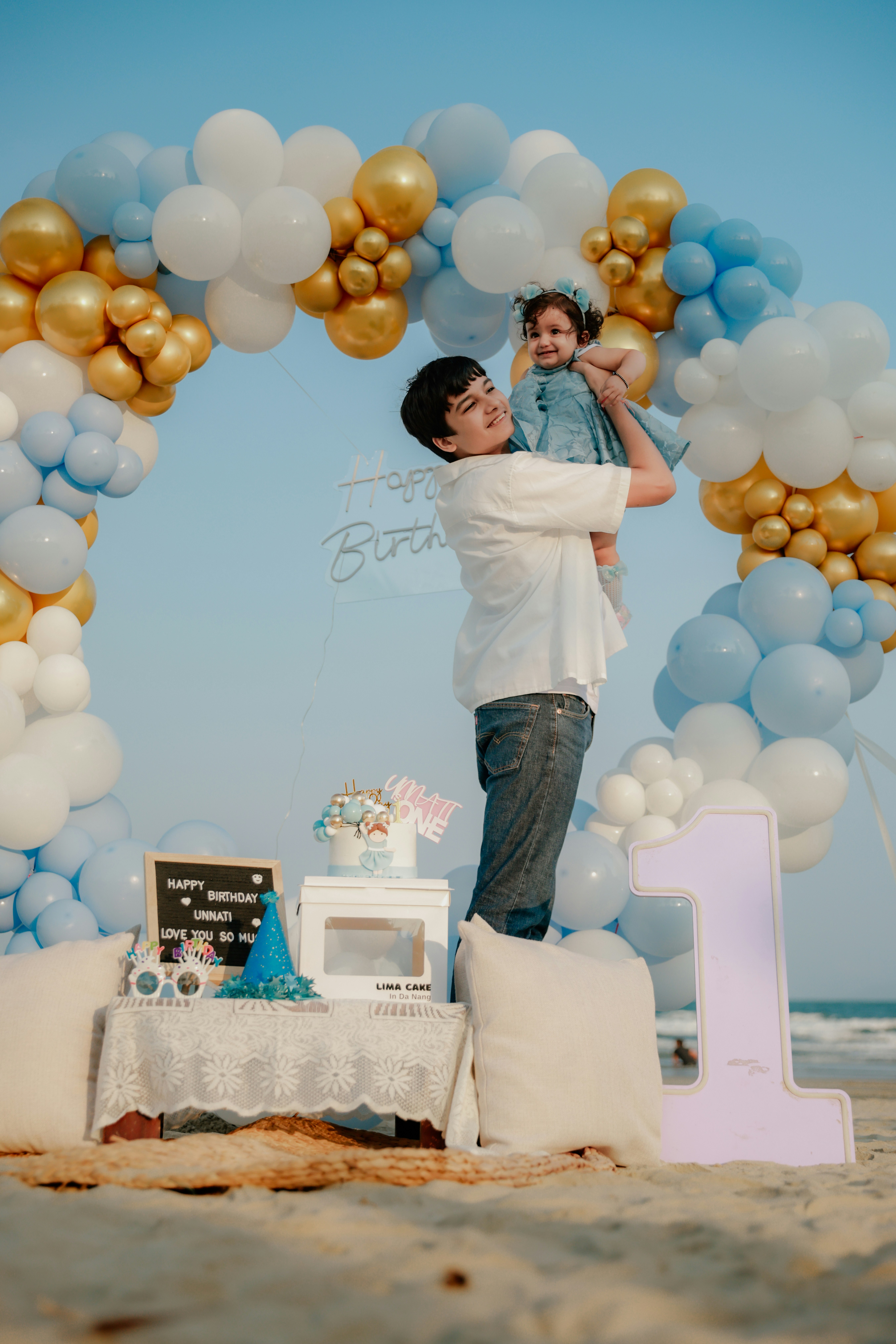 Joyful Father Lifts Birthday Baby Under a Balloon Arch on the Beach
