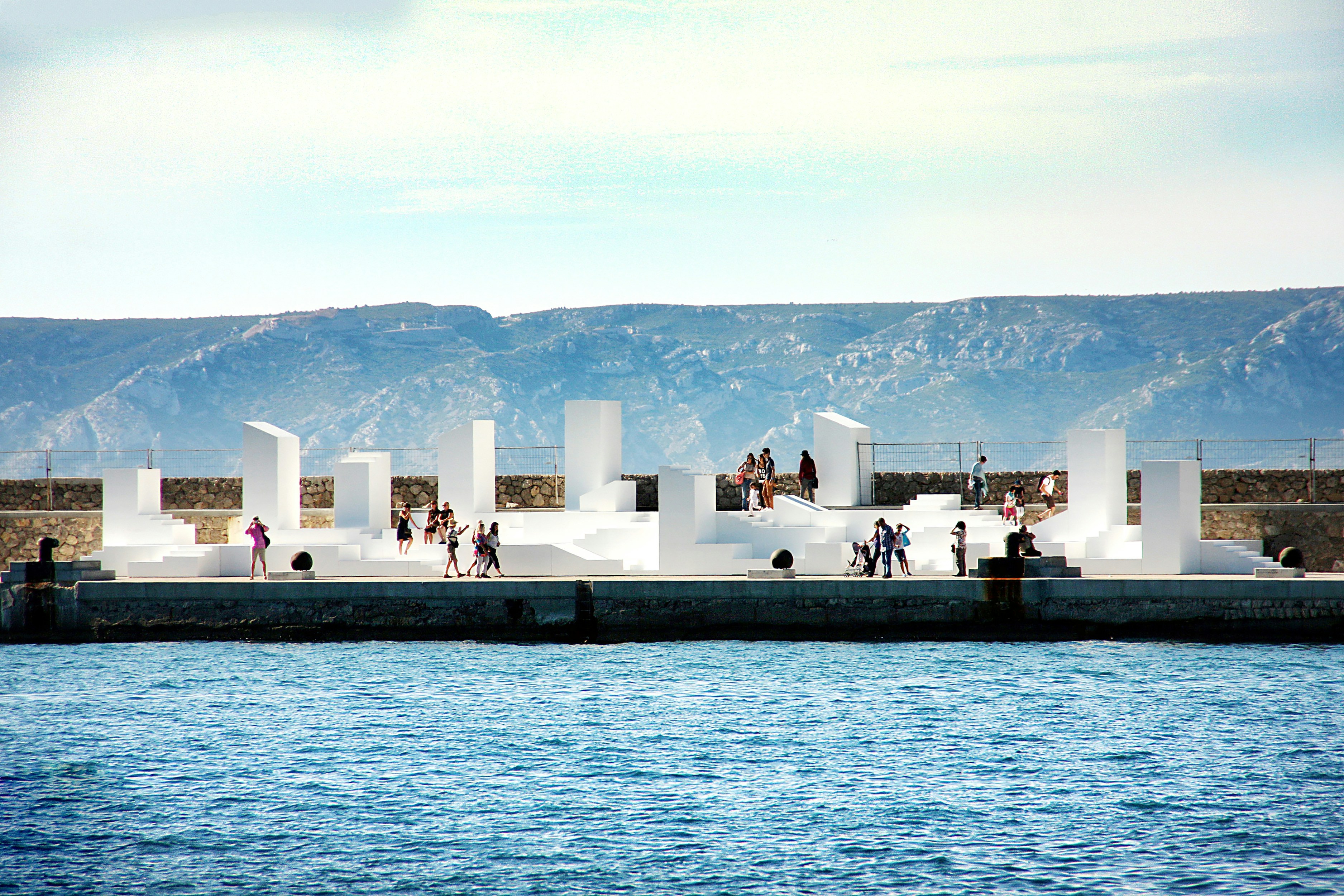 White geometric pier sculptures under a distant mountain range by the sea