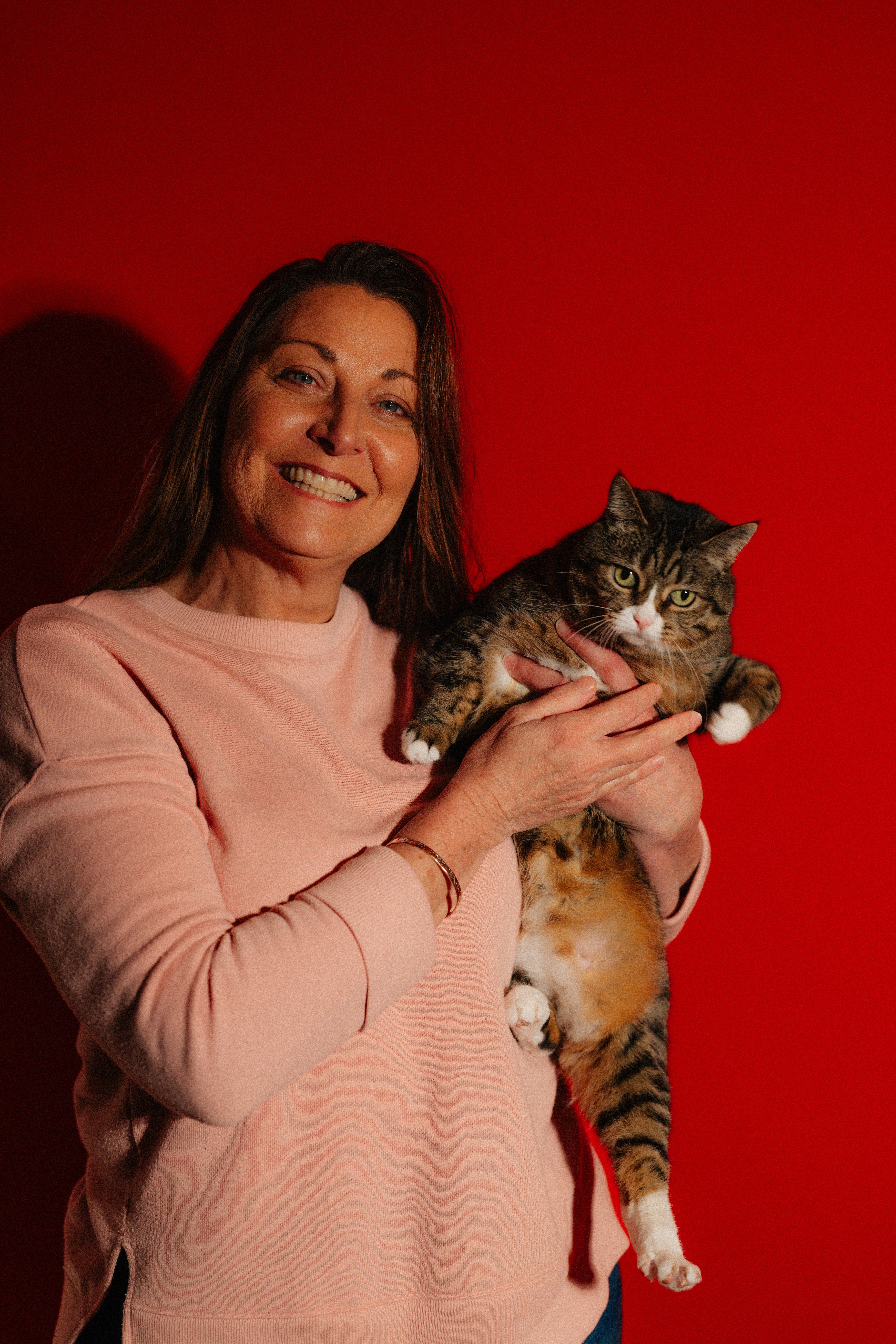Smiling guardian with a grinning tabby against a crimson backdrop