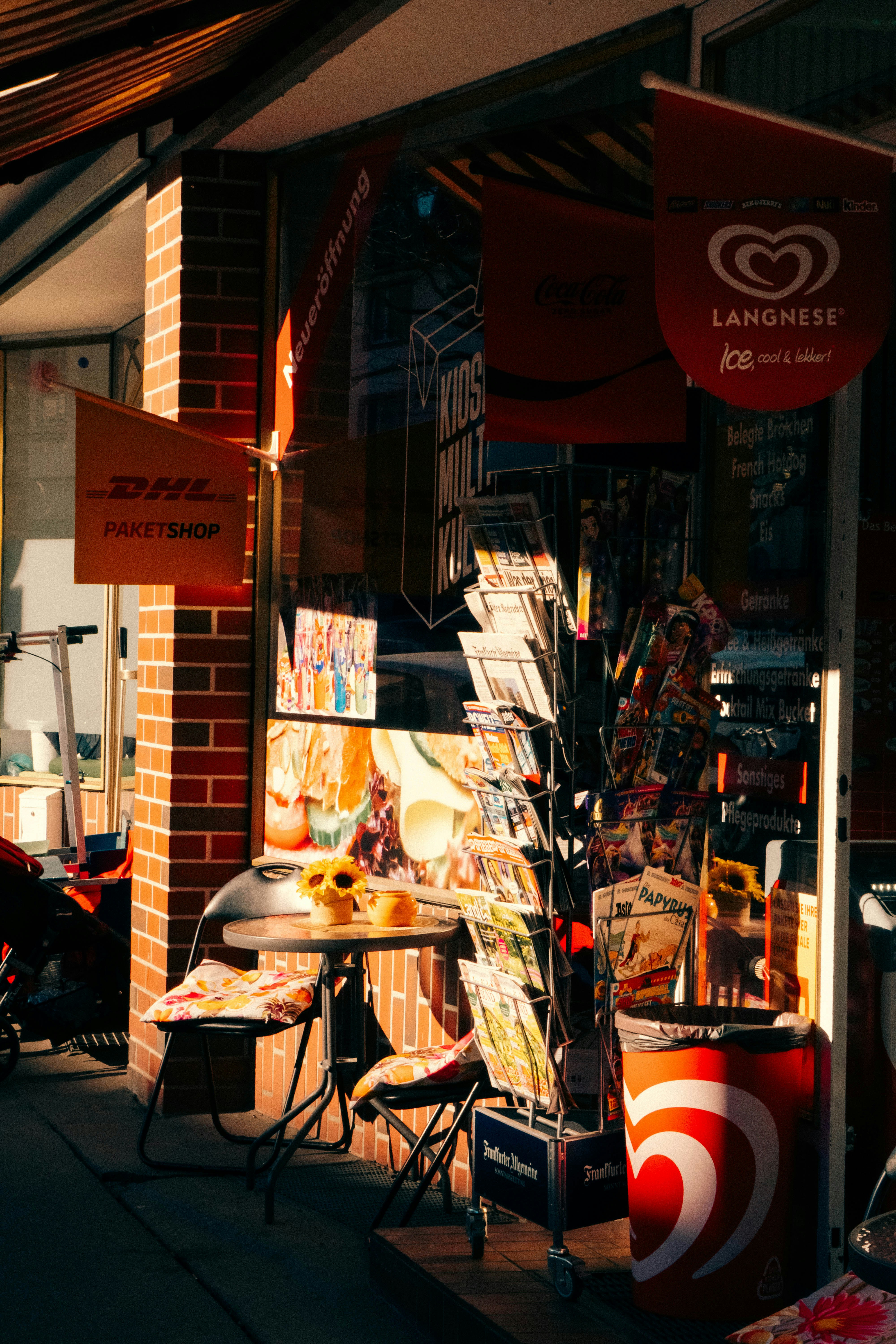 Sunlit Alleyfront Café: A Street-side Newsstand and Flowered Table