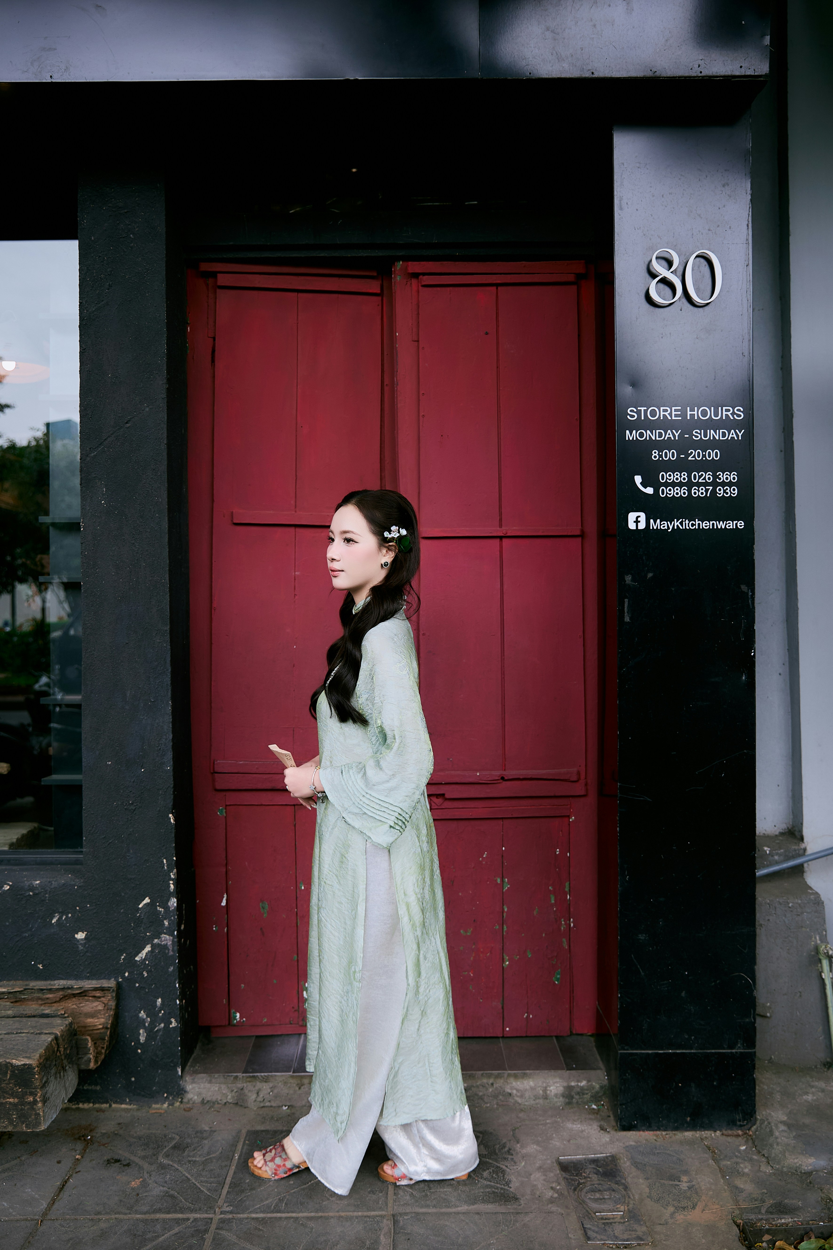 Girl in a mint áo dài steps away from the red door under a numbered storefront