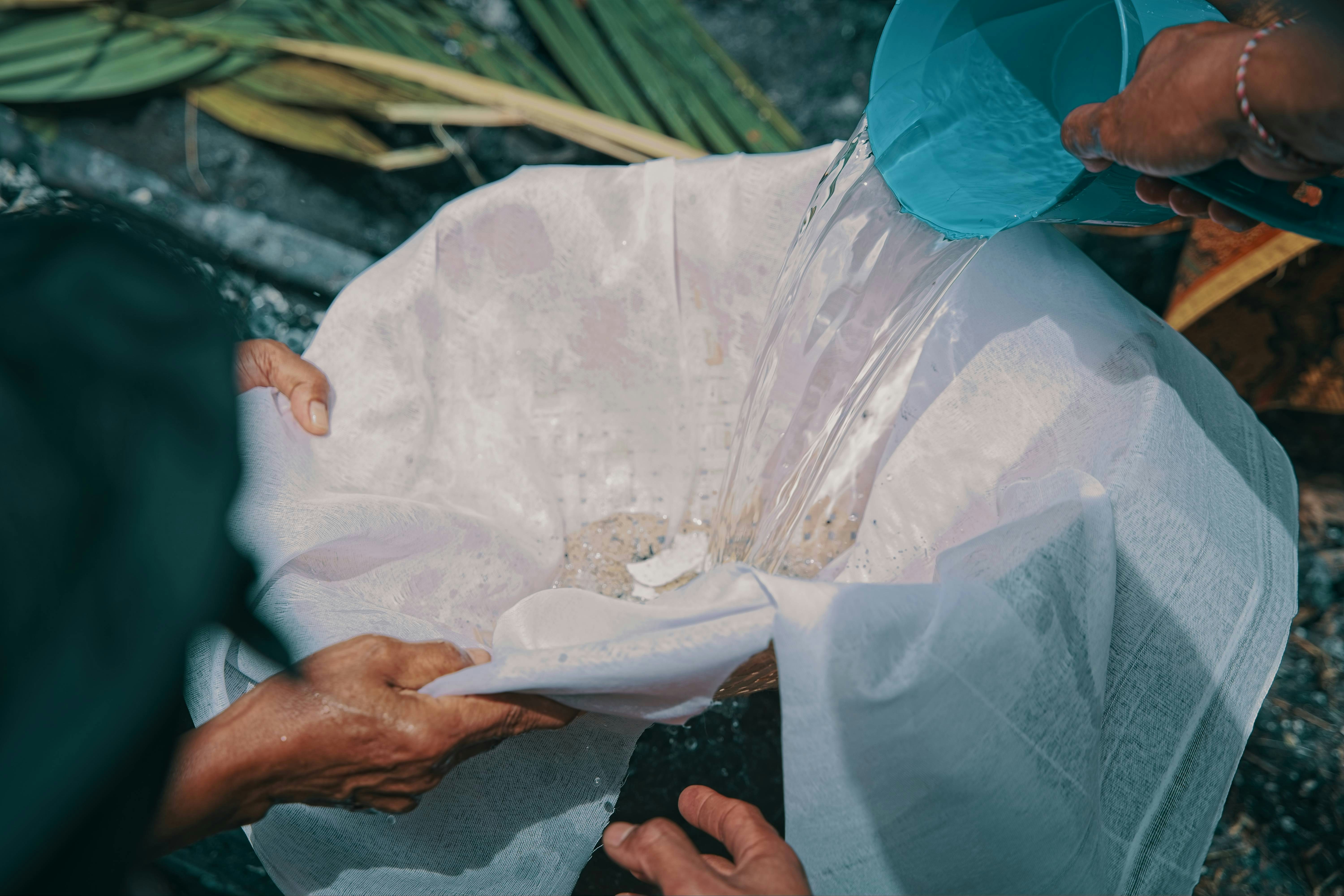 Hands Pouring into a White Fabric Scoop: A Close-Up of a Wet Task