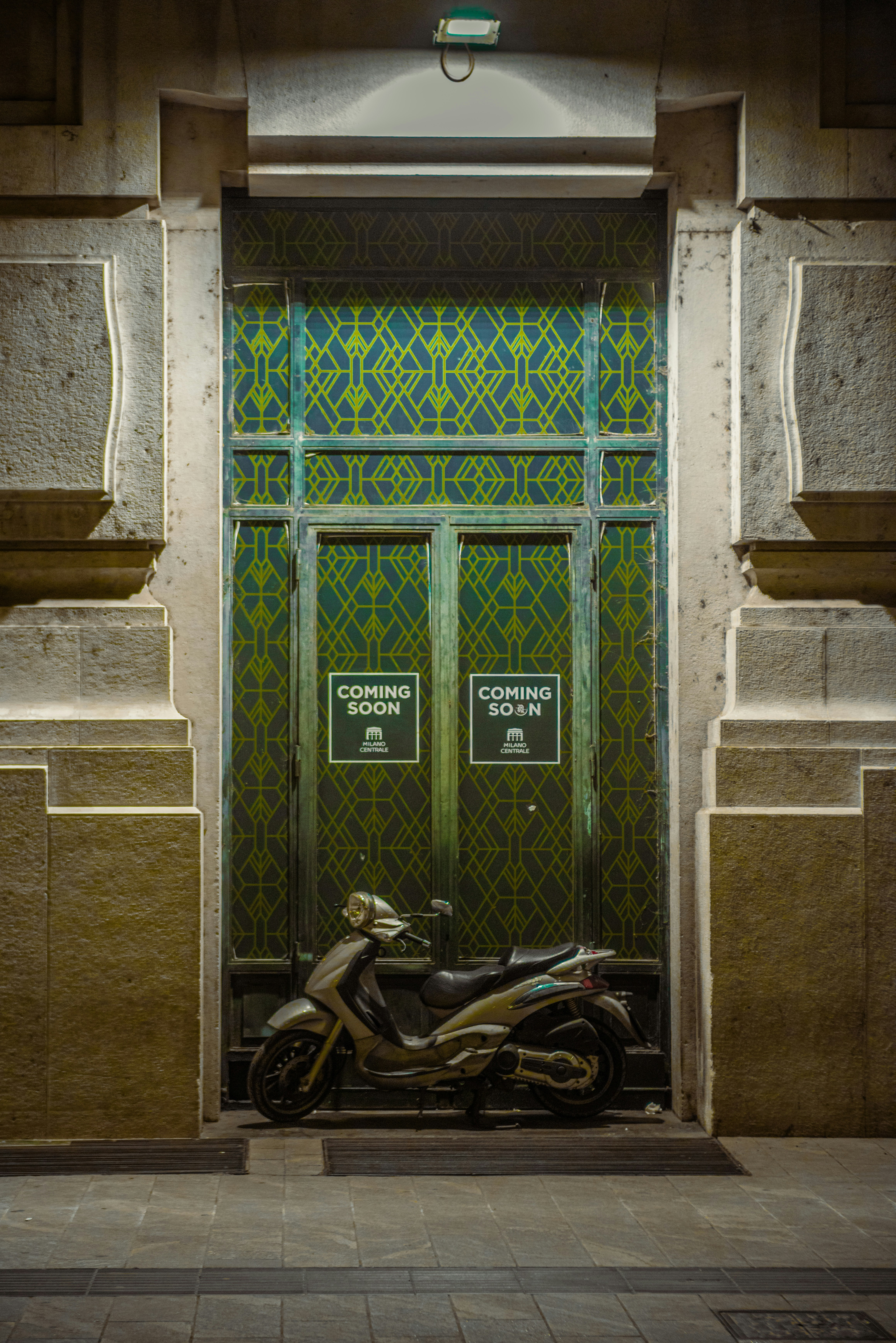 Green patterned doorway under urban arch frames a lone scooter