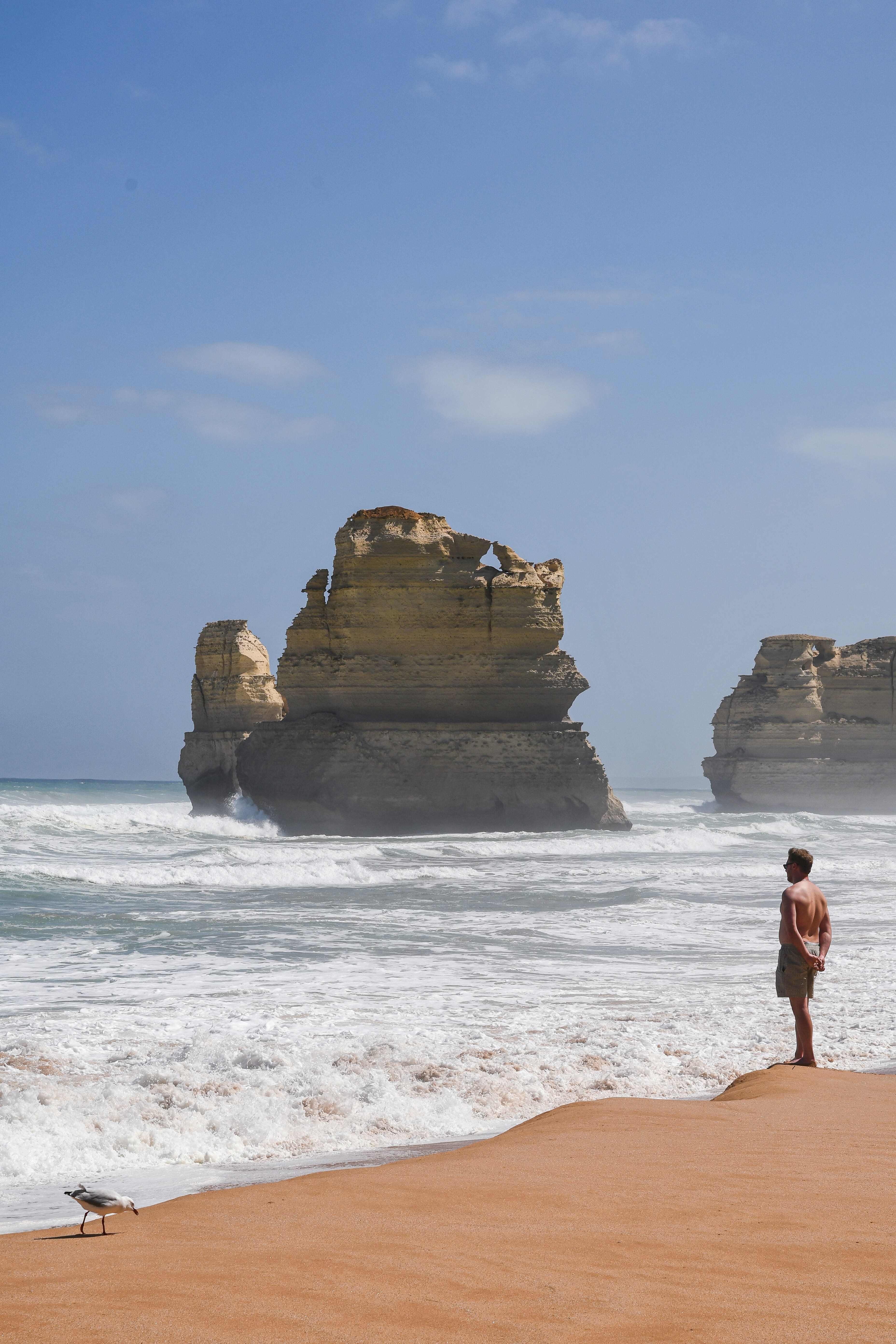 Coastline Witness: A Seaside Figure and Eroded Monoliths under Wide Blue