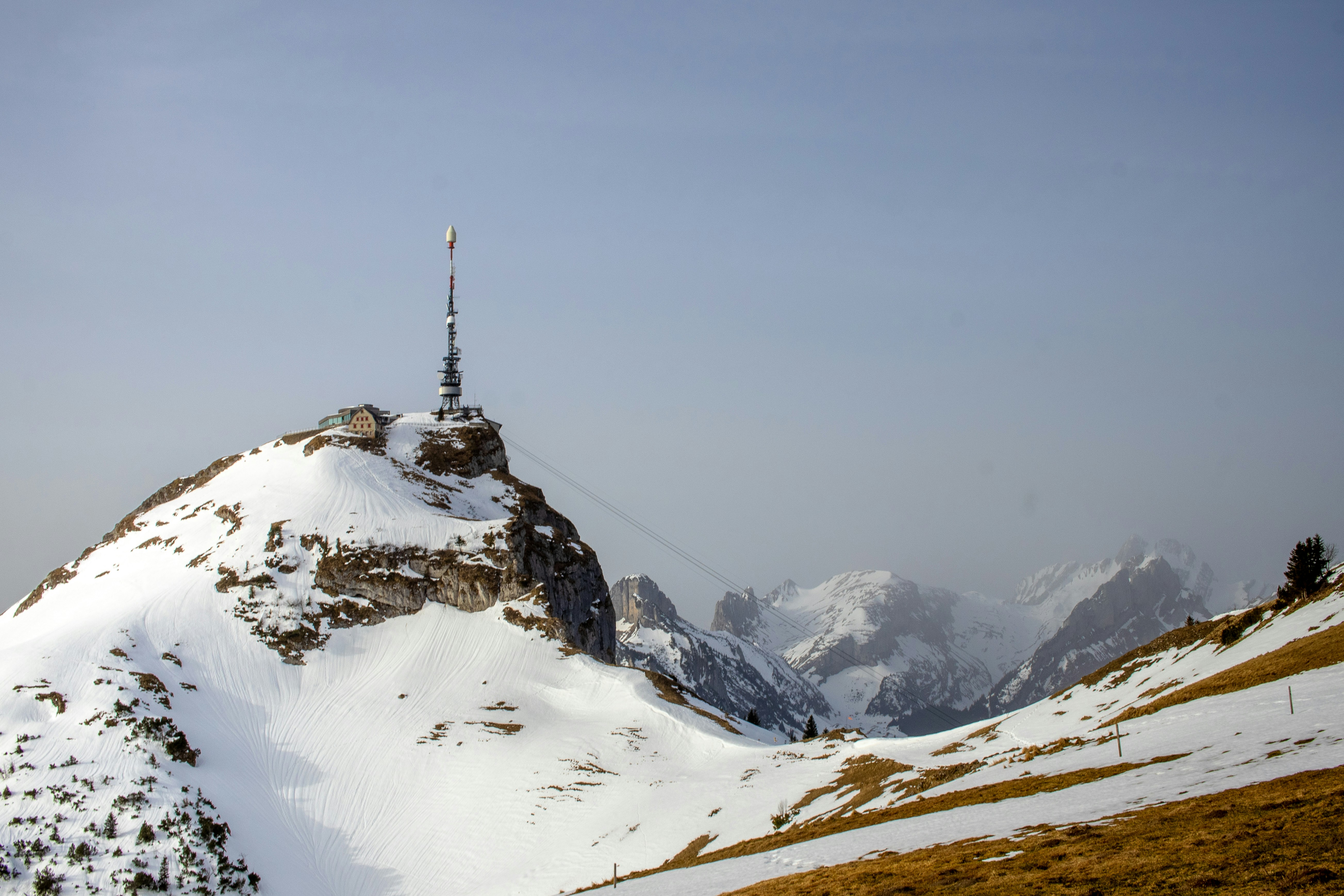 Snow-crowned hilltop with a distant antenna against a pale alpine horizon