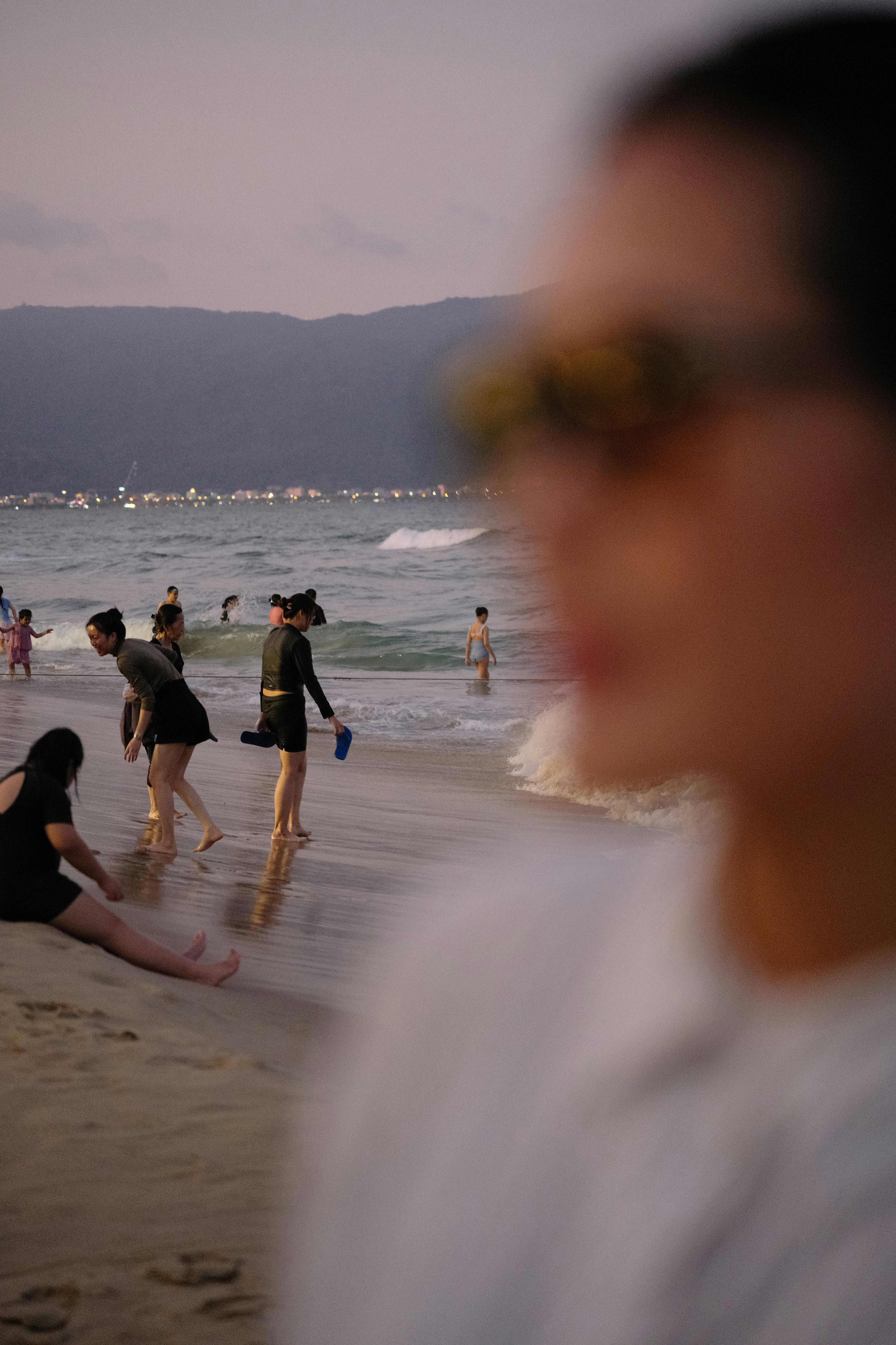 Blurry Foreground, Busy Shoreline: A Sunset Beach Scene with People in Calm Tide
