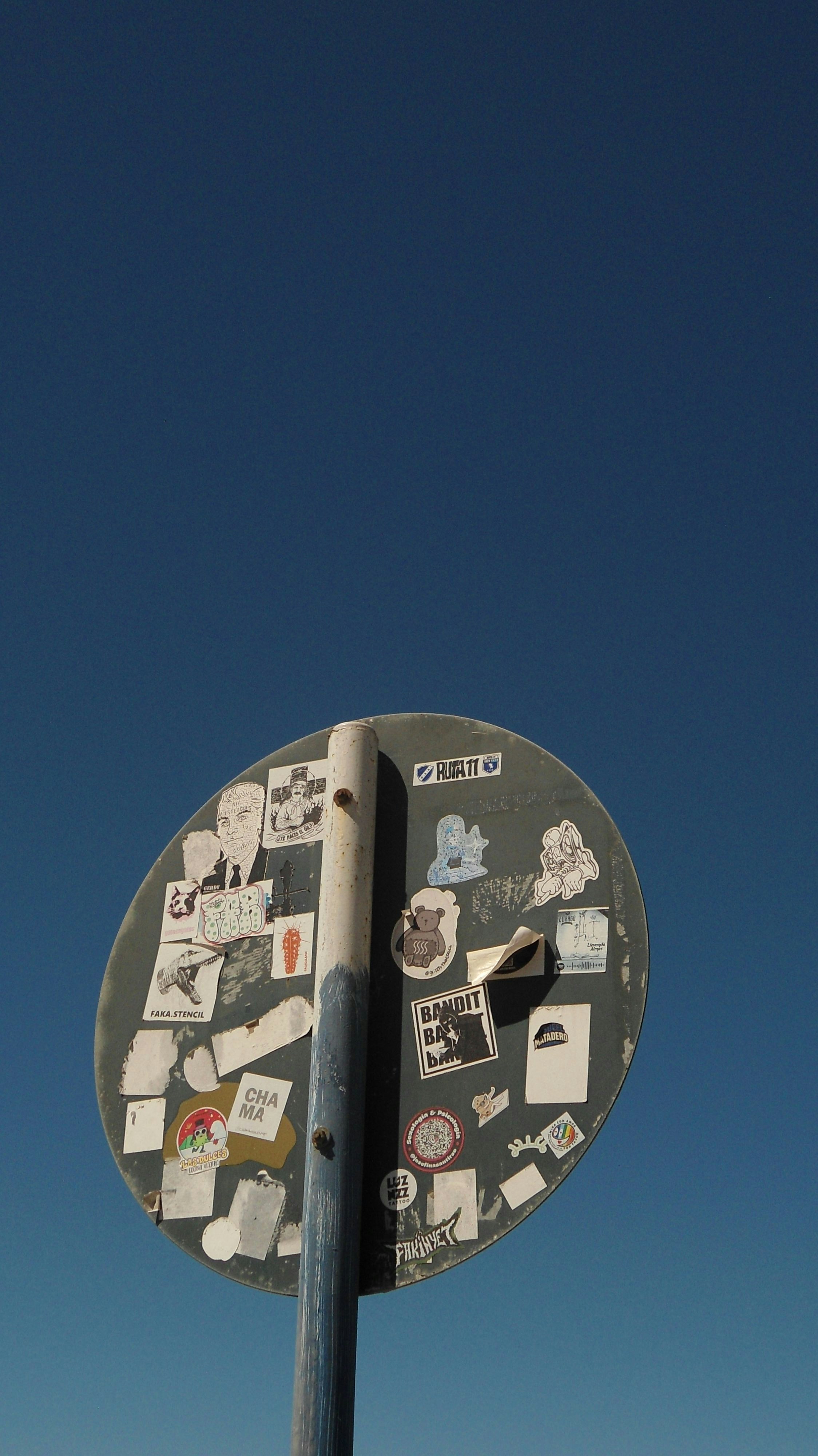 Round sign covered in stickers against blue sky