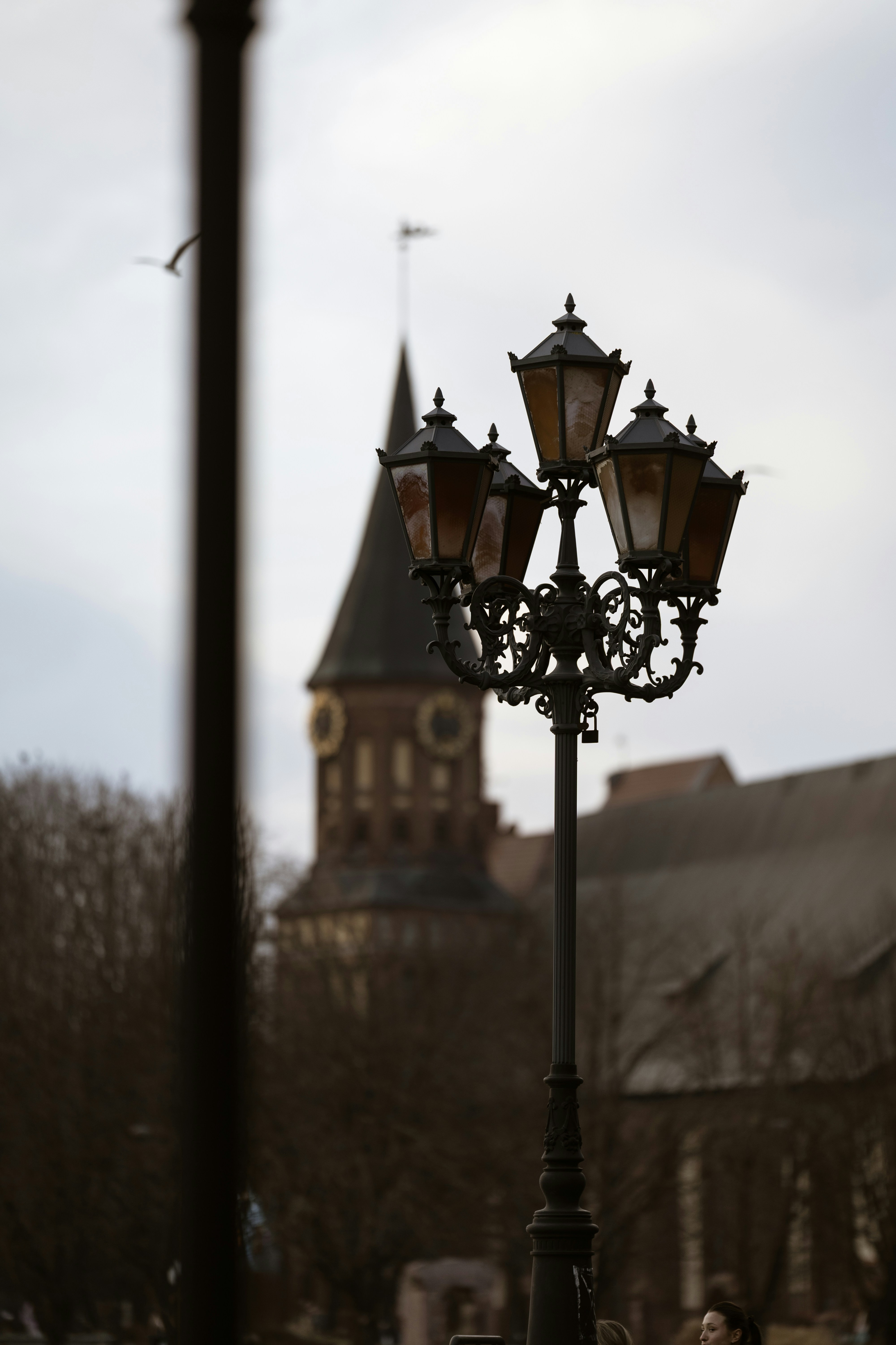 A vintage cast-iron street lamp stands in the foreground with the silhouette of a clock tower behind. Kaliningrad Cathedral on Kant Island.