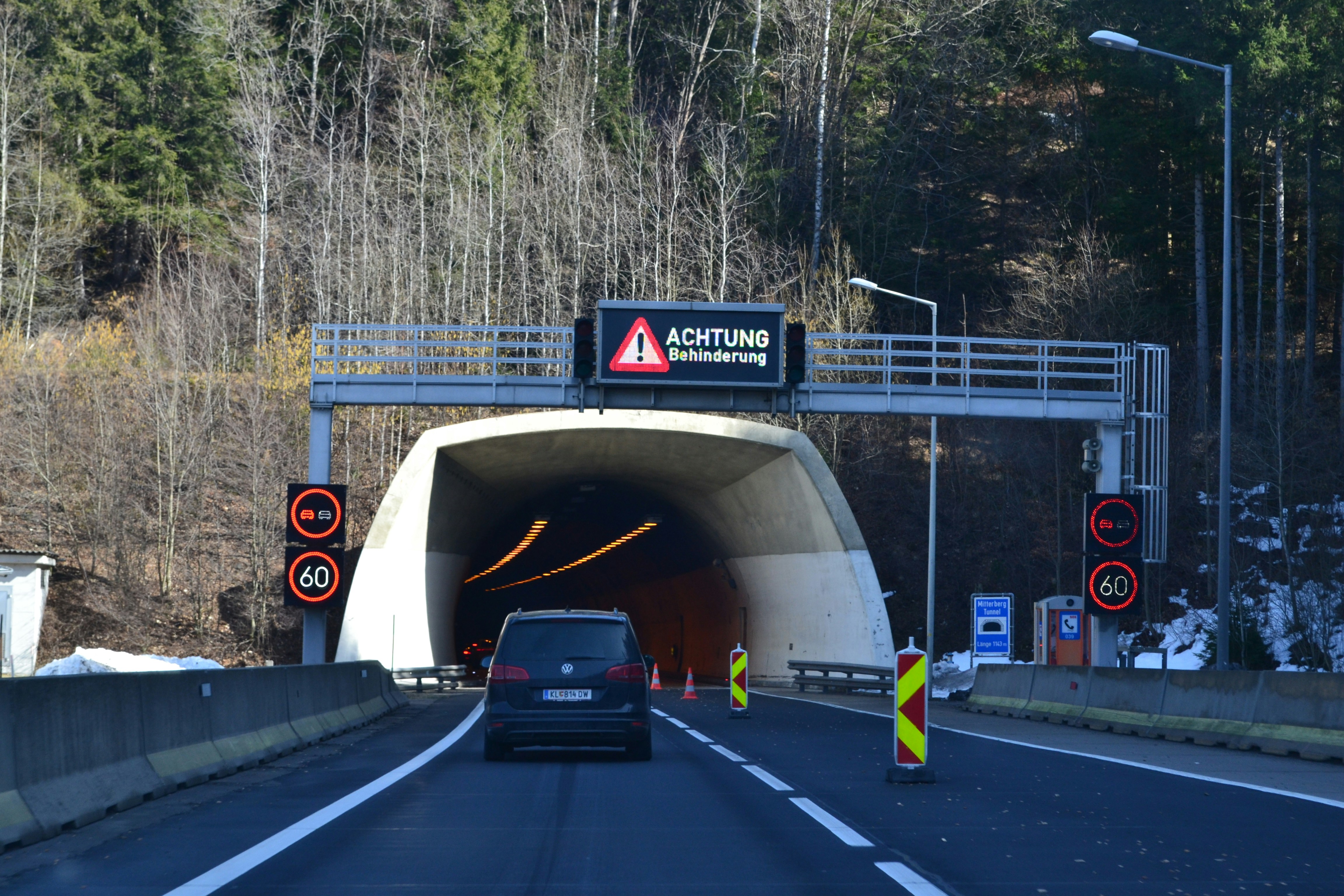 Tunnel Entrance on a Snowy Highway with Signage and Car in Transit