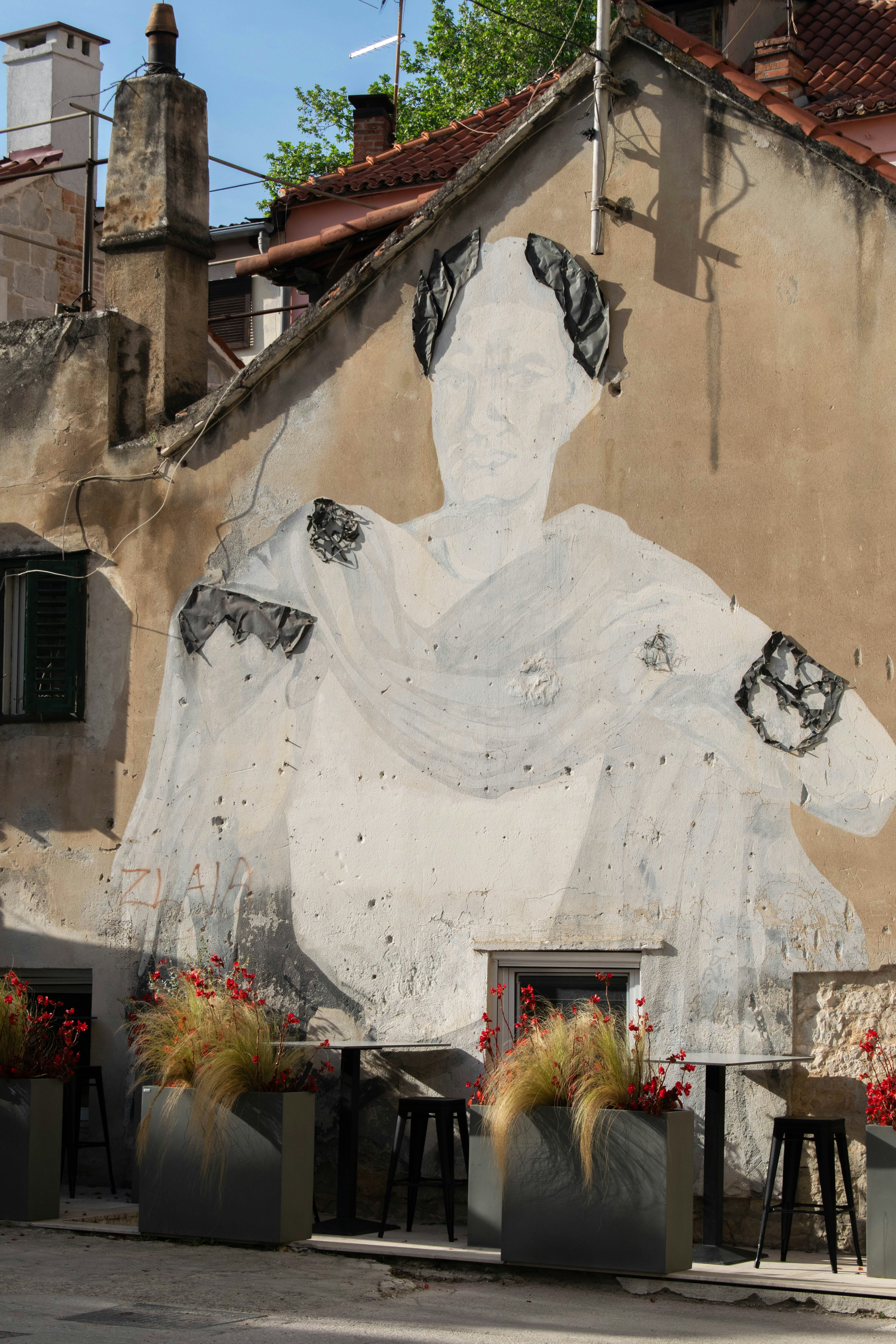 Graffiti mural of a pale figure on a sunlit villa wall