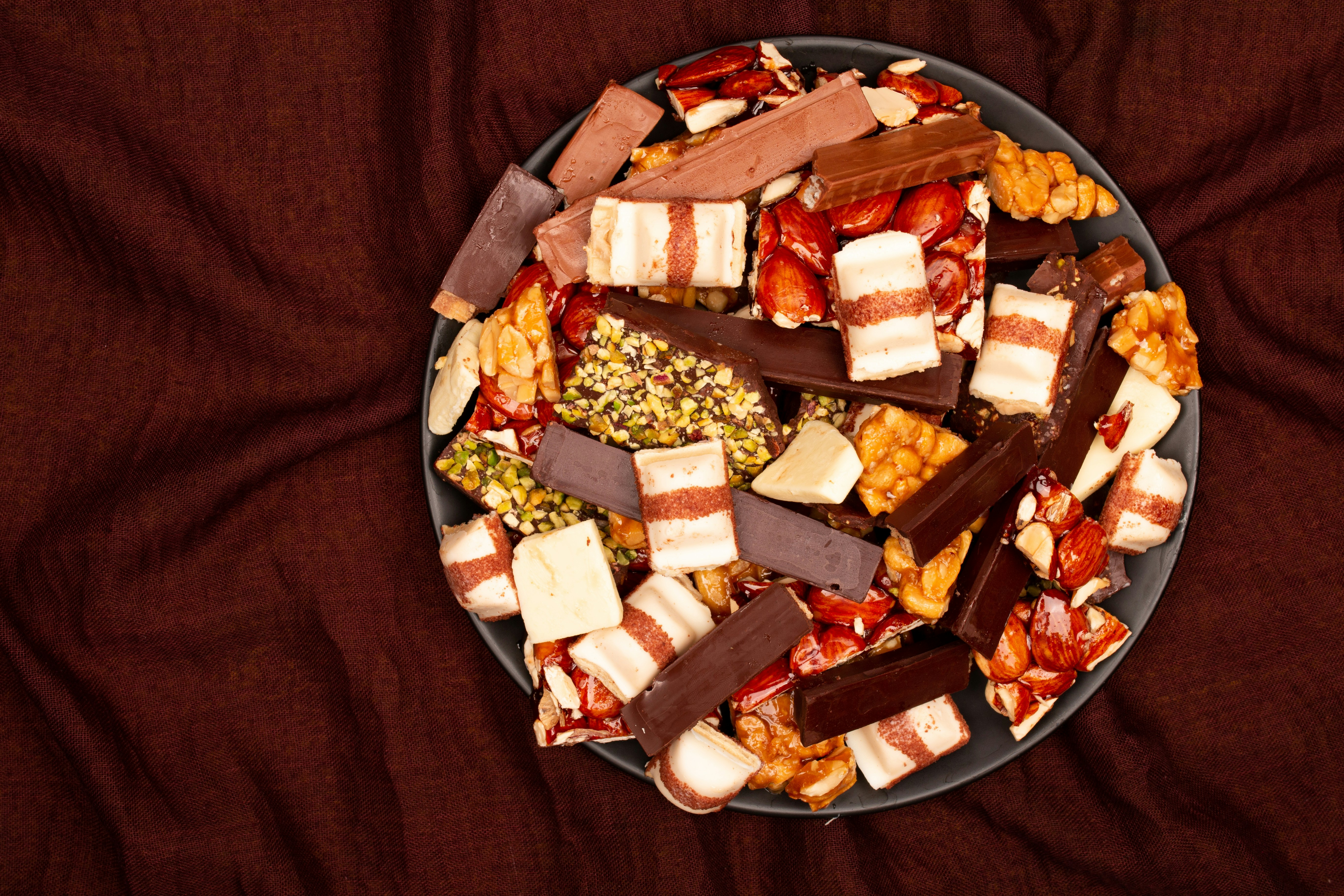 Assorted chocolate bars and pastries arranged on a platter against a dark maroon backdrop