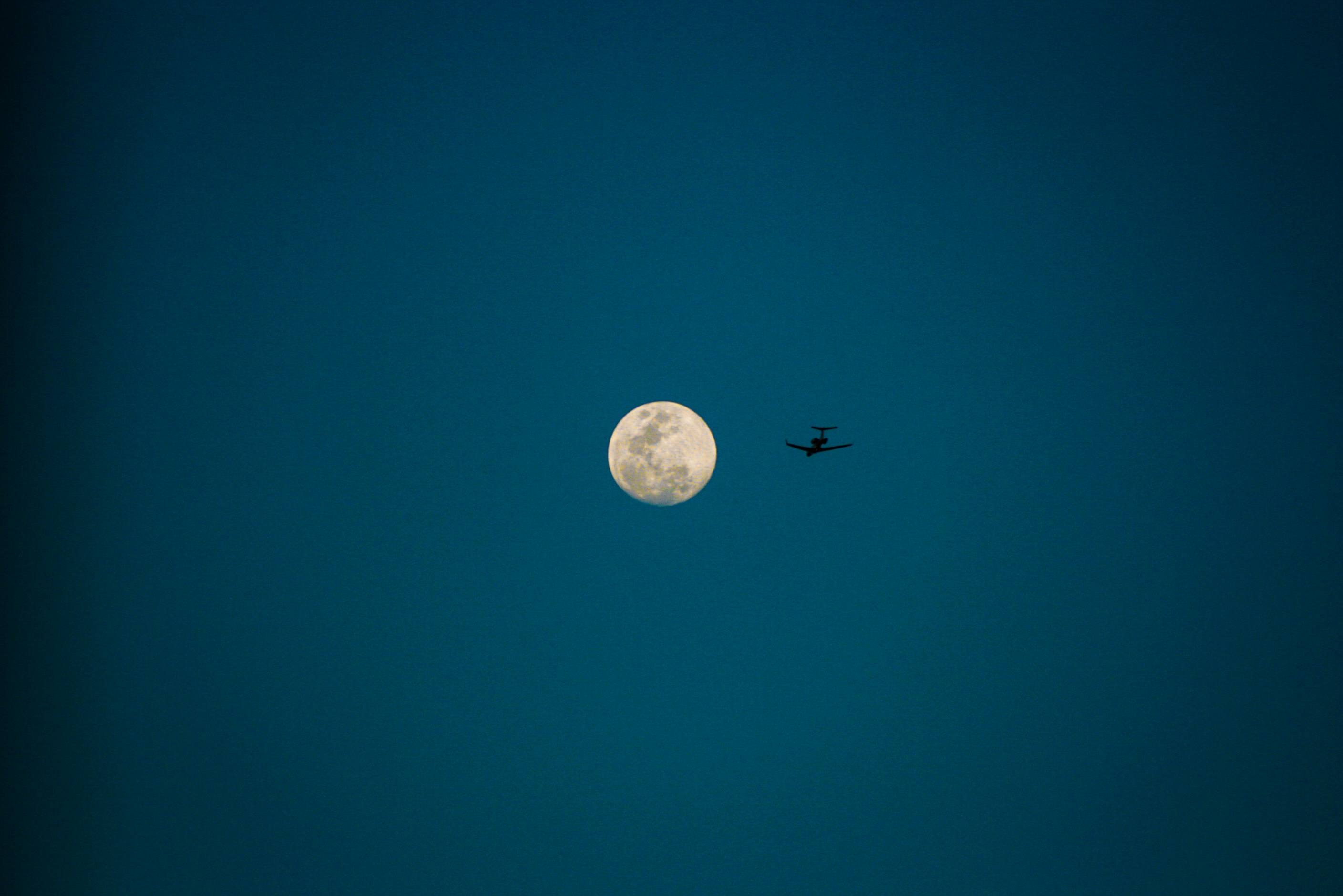 Moonlit Silhouette: lone aircraft gliding past a pale satellite