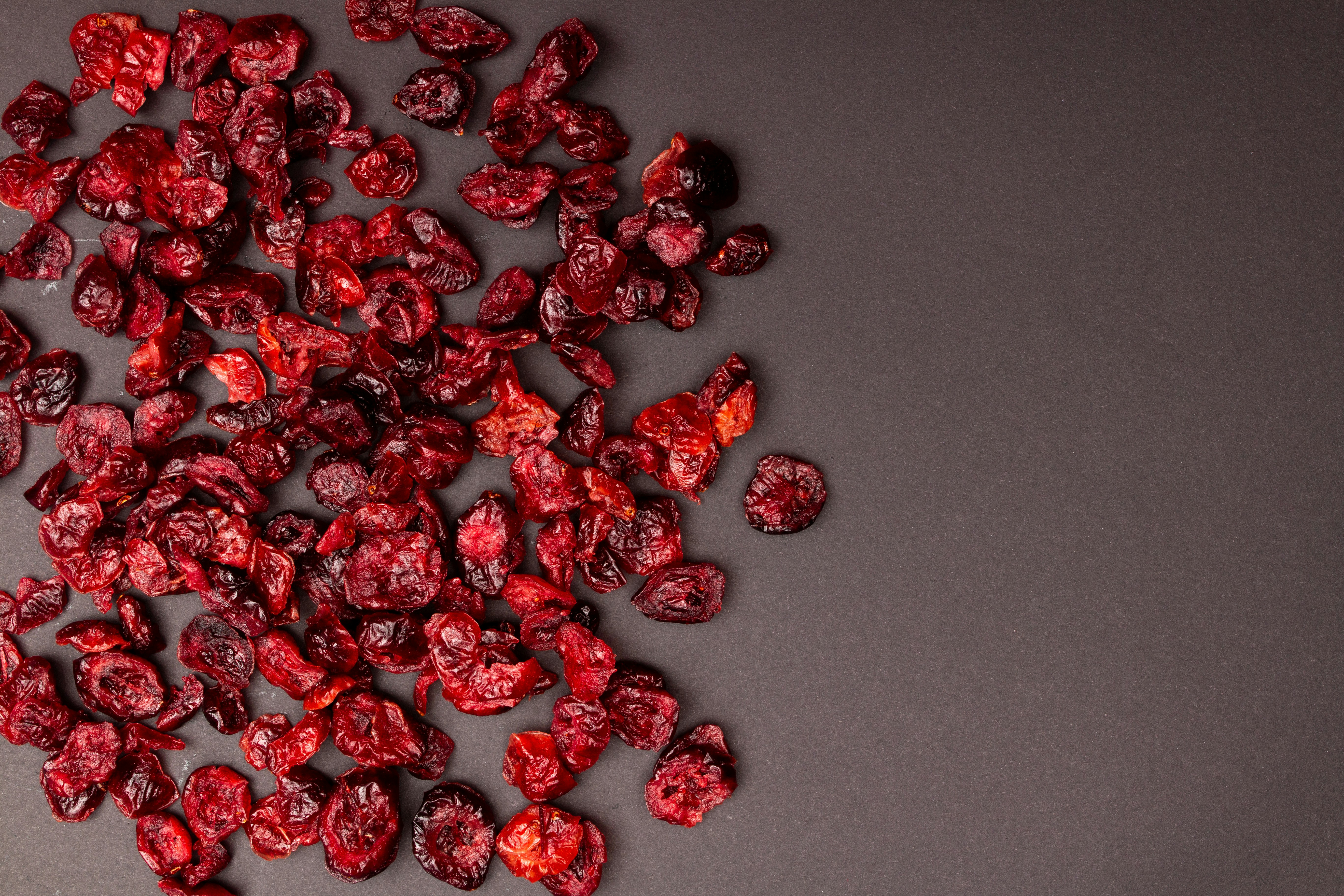 Cluster of dried red berries spread across a dark flat surface with soft lighting and subtle texture in the background.
