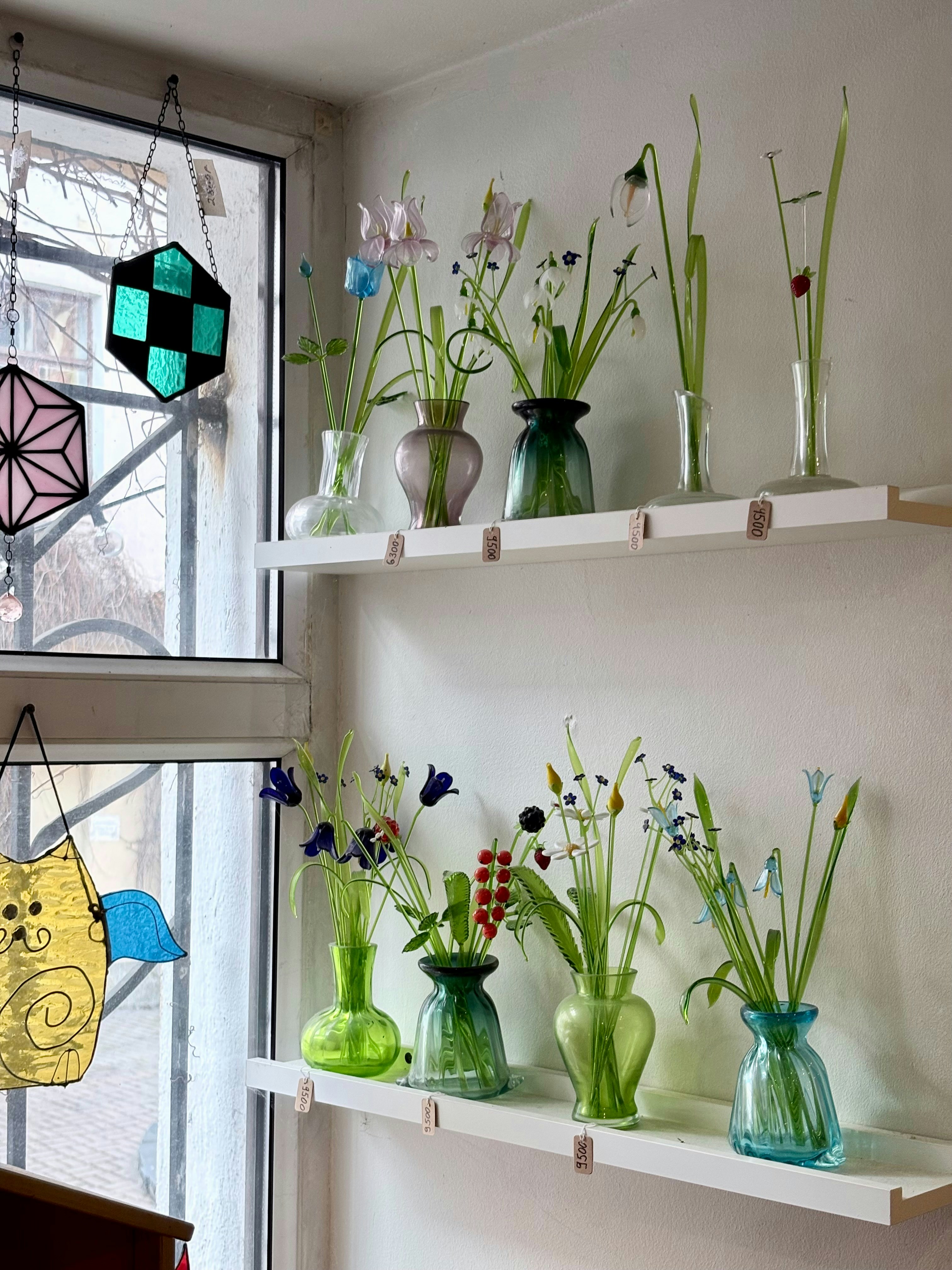 Glass vases with delicate flowers on shelves near window.