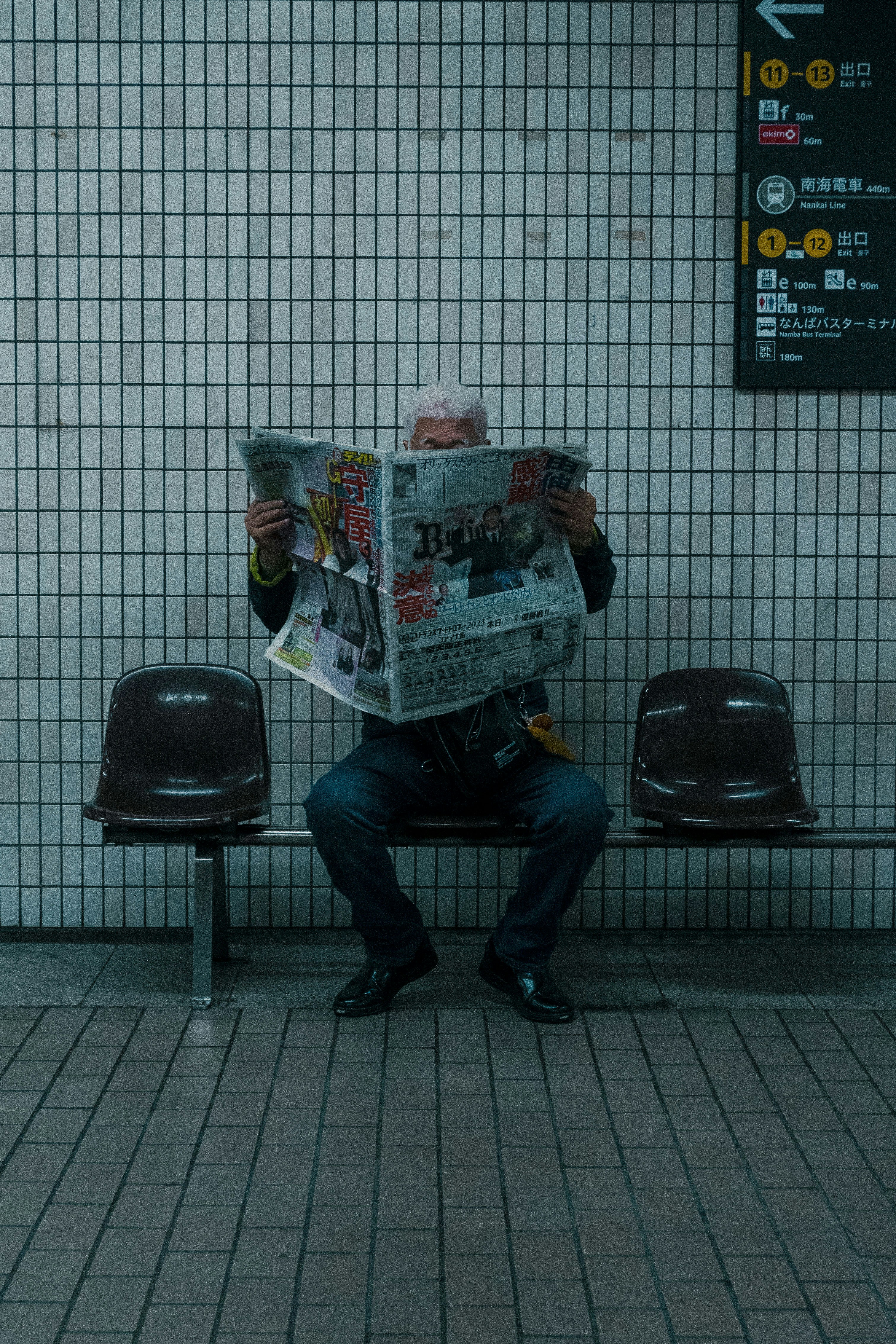 Man reading newspaper on a bench at a station