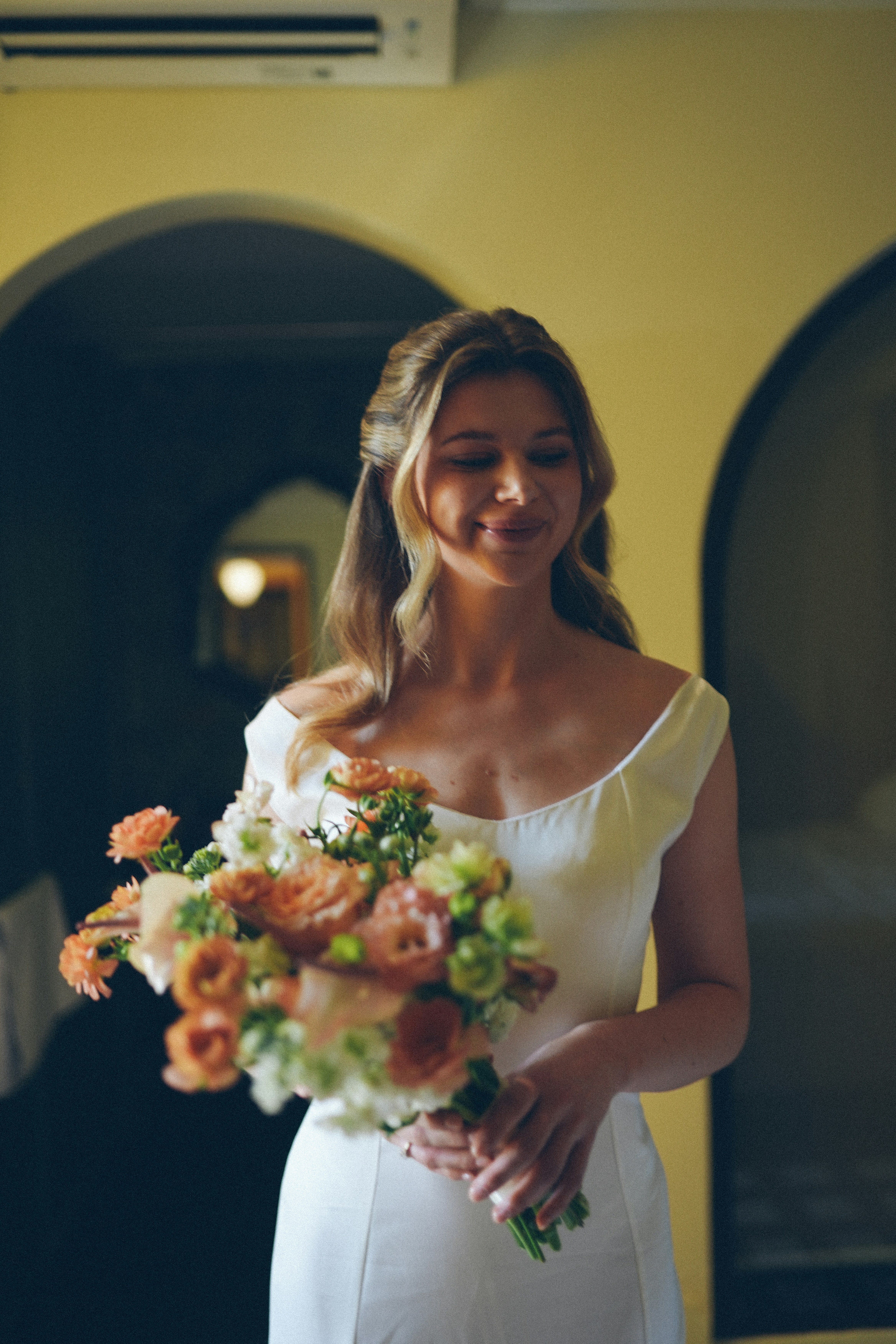 Bride with bouquet beneath warm arches