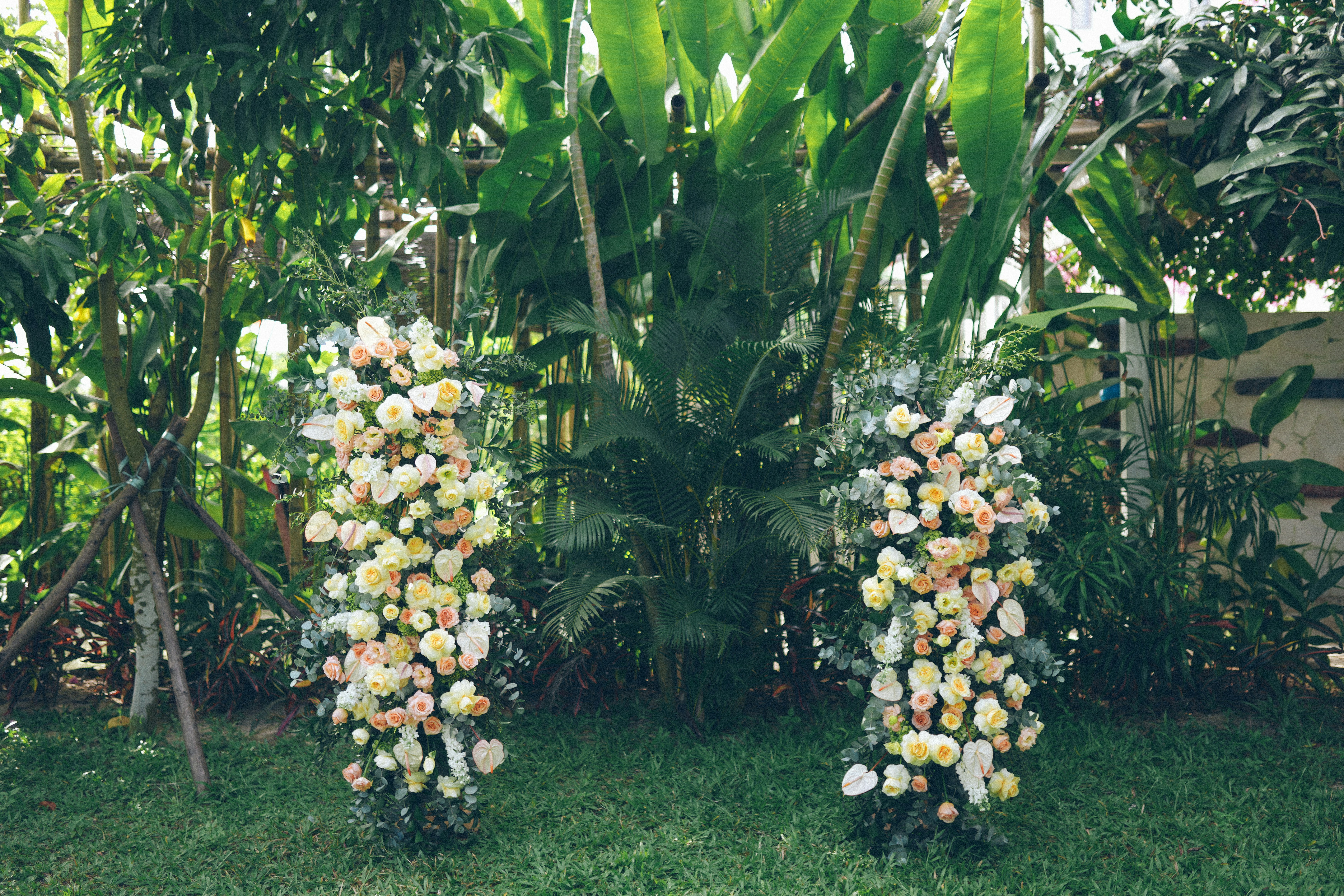 Two vertical champagne-and-cream floral columns in a tropical garden ceremony