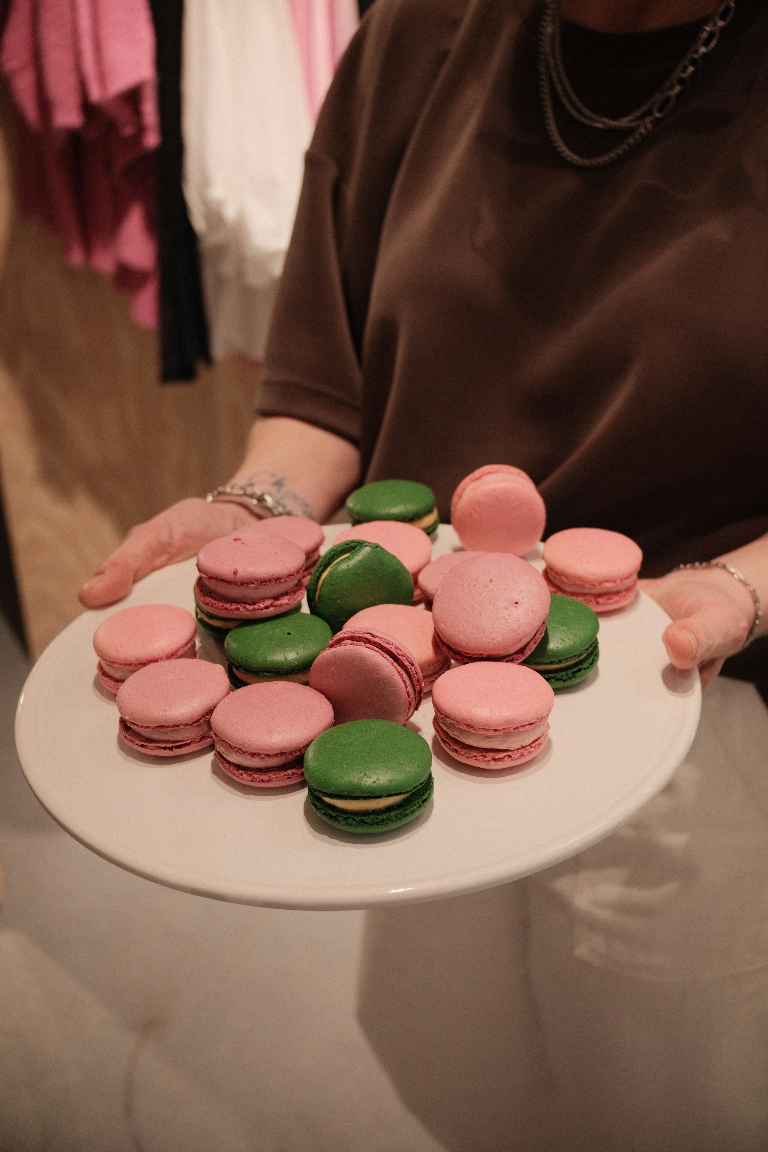Plate of pink and green macarons carried by a person in a brown top