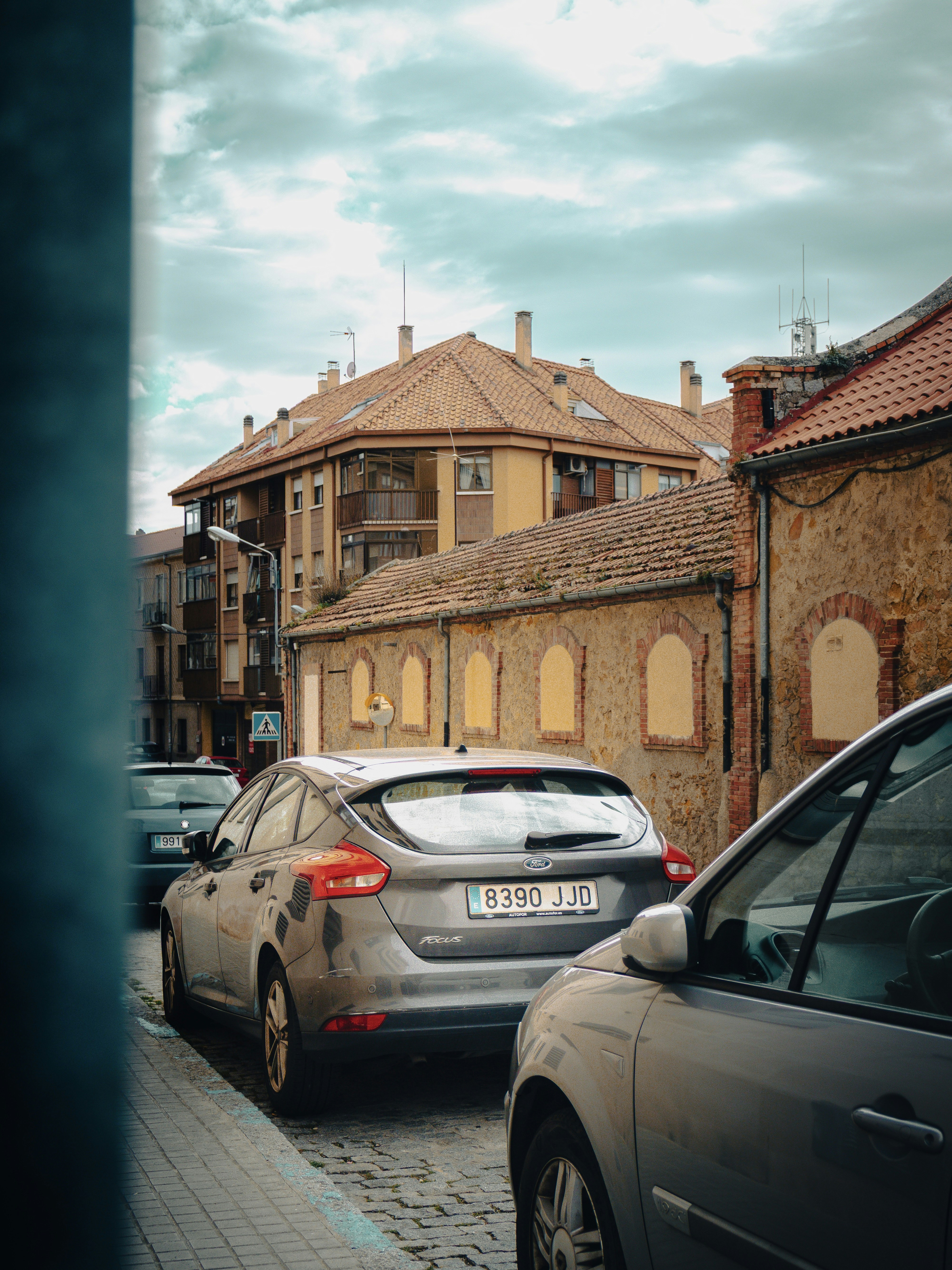 Urban Carline: A narrow street framed by weathered brick and parked hatchbacks