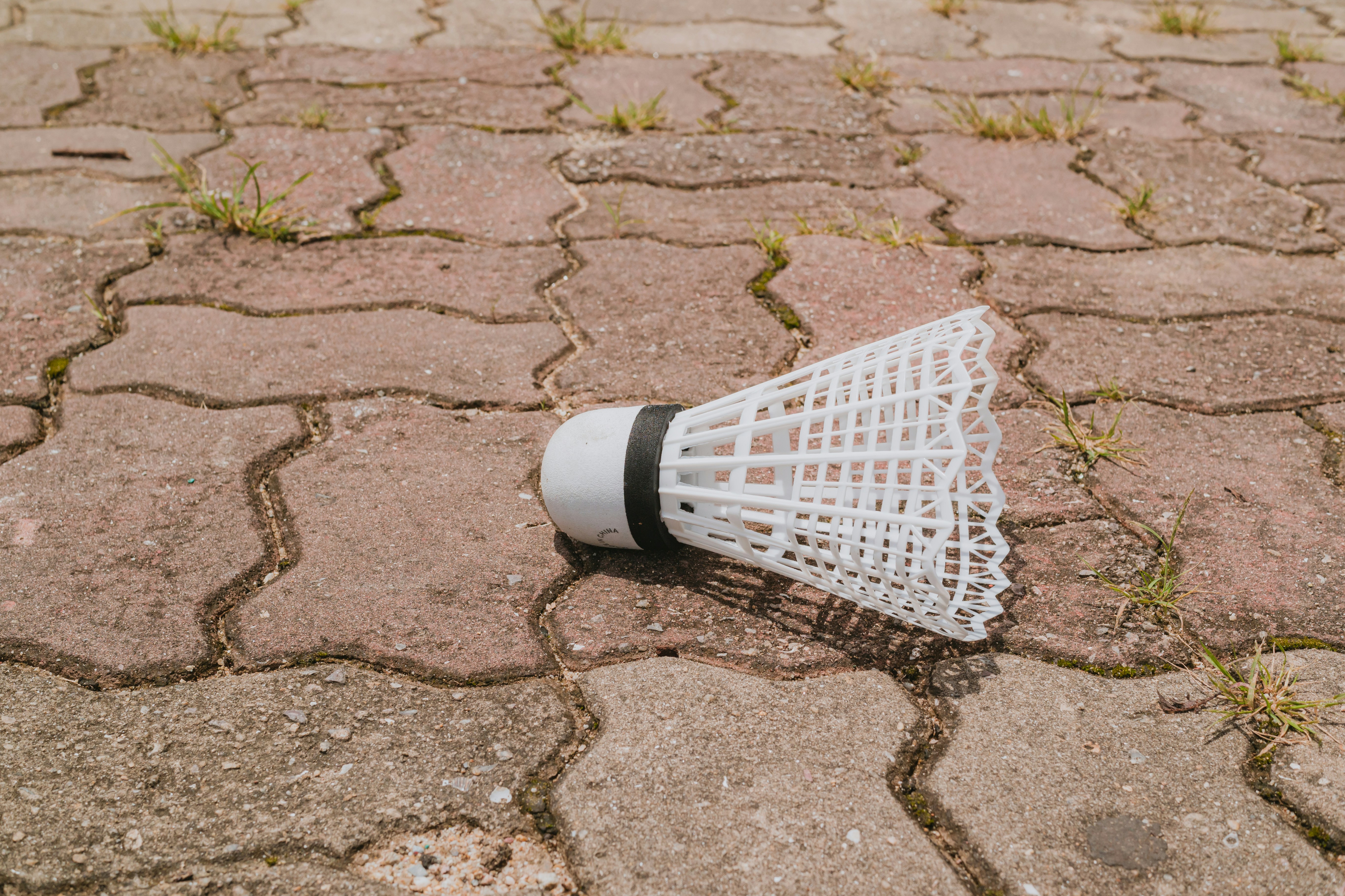 A white shuttlecock rests on a brick pathway.
