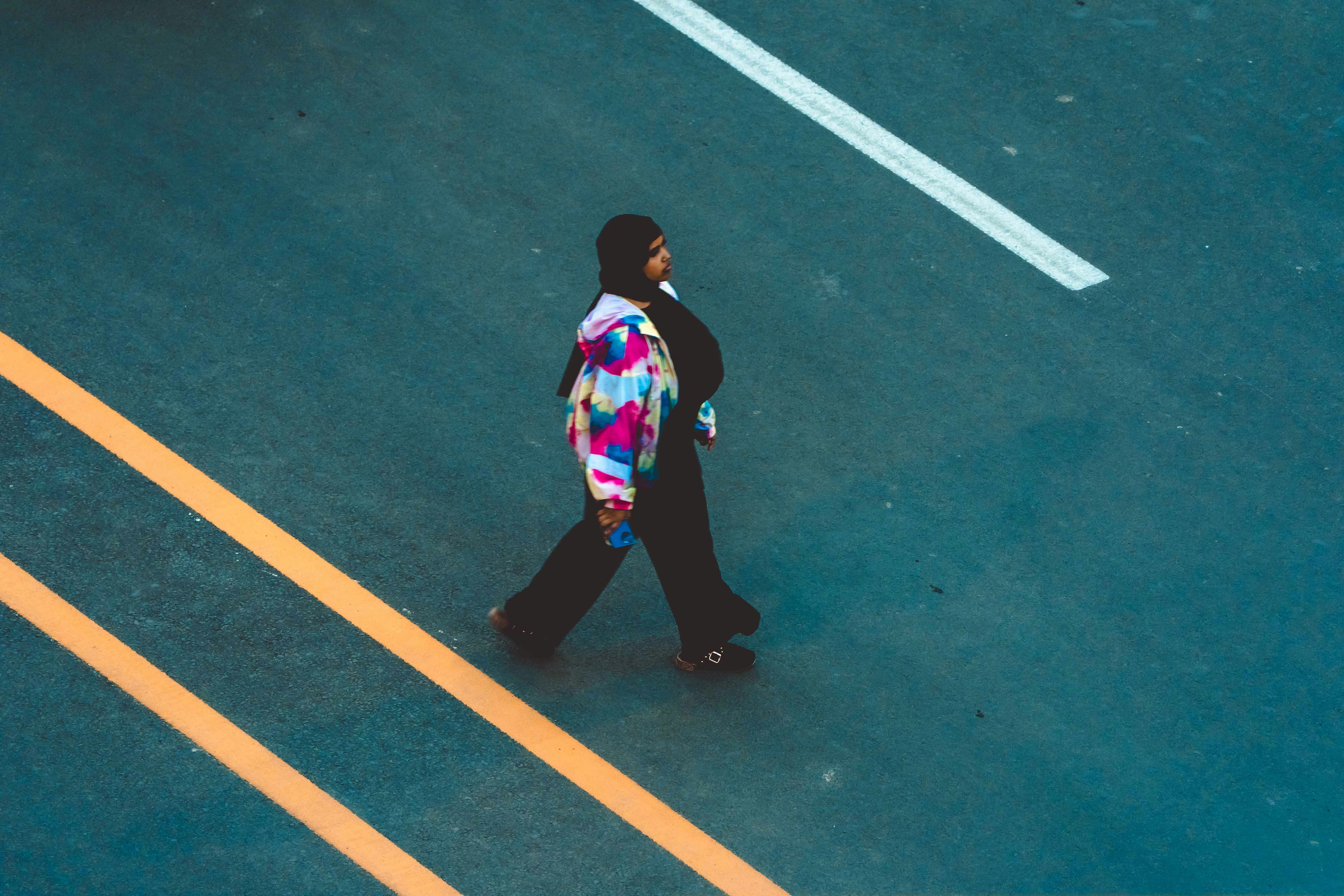 A person walks across a street with yellow lines.