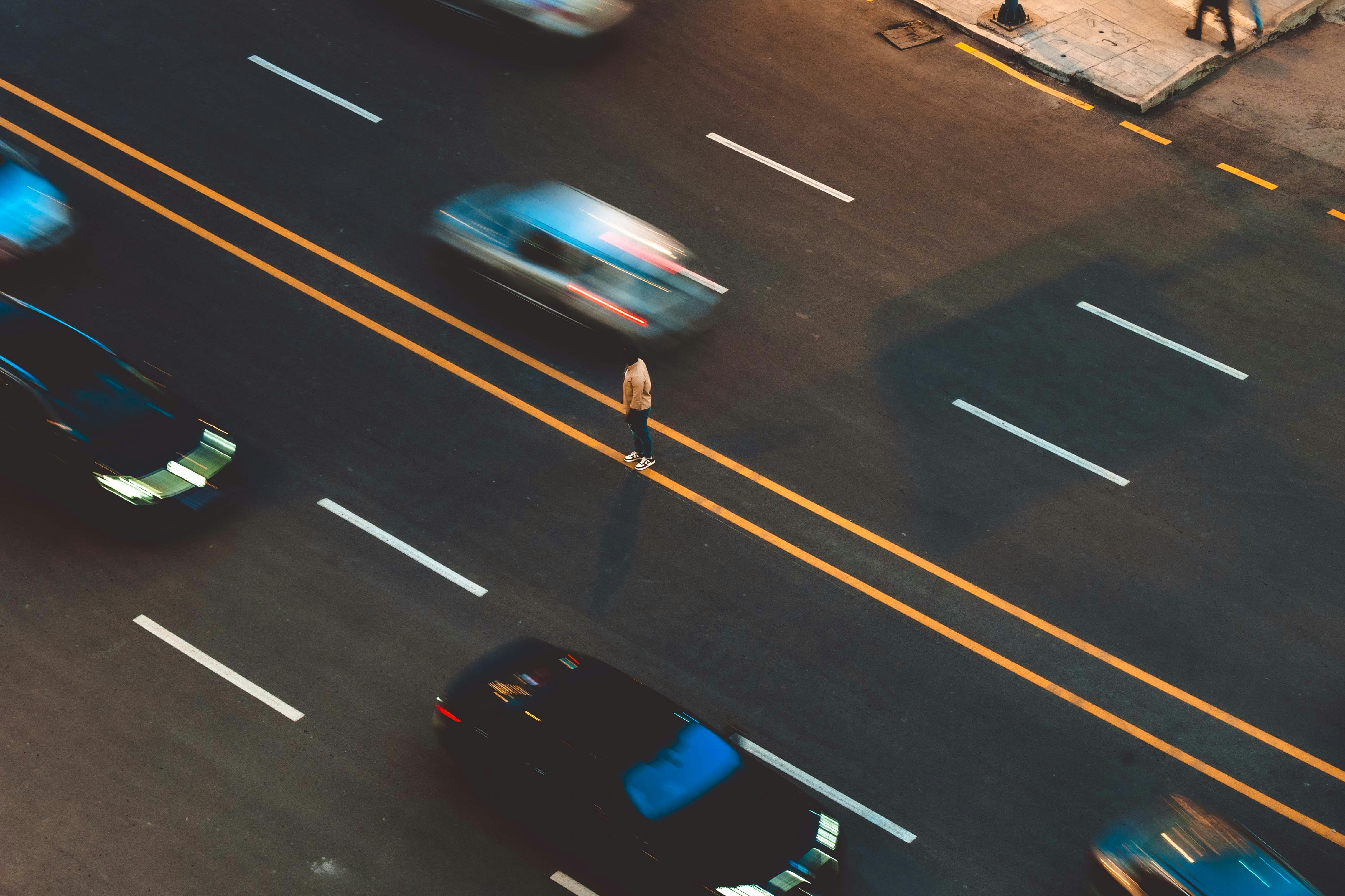 A lone person stands on a busy street with cars.