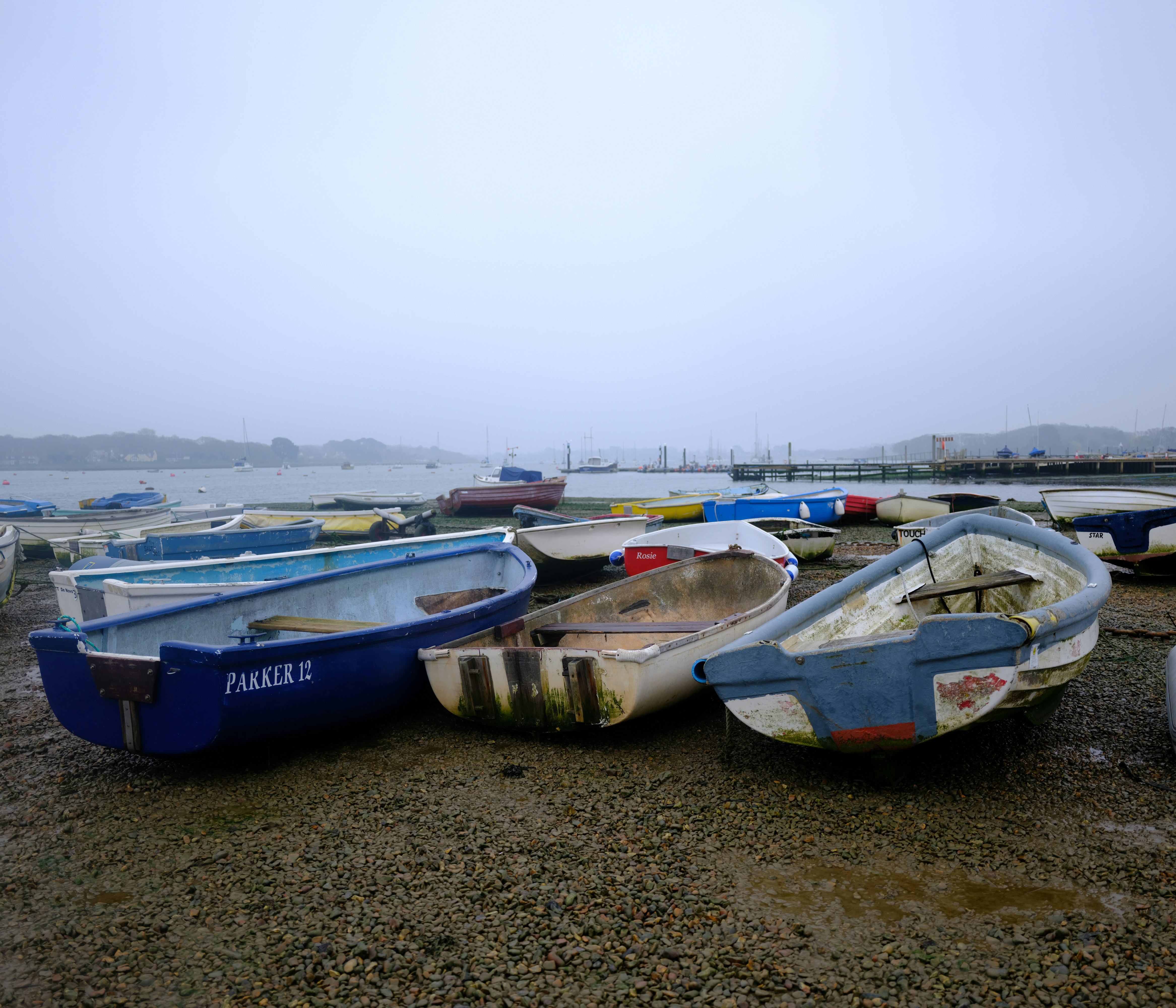 Dockside Palette: Weathered Boats Rests on a Pebble Shore