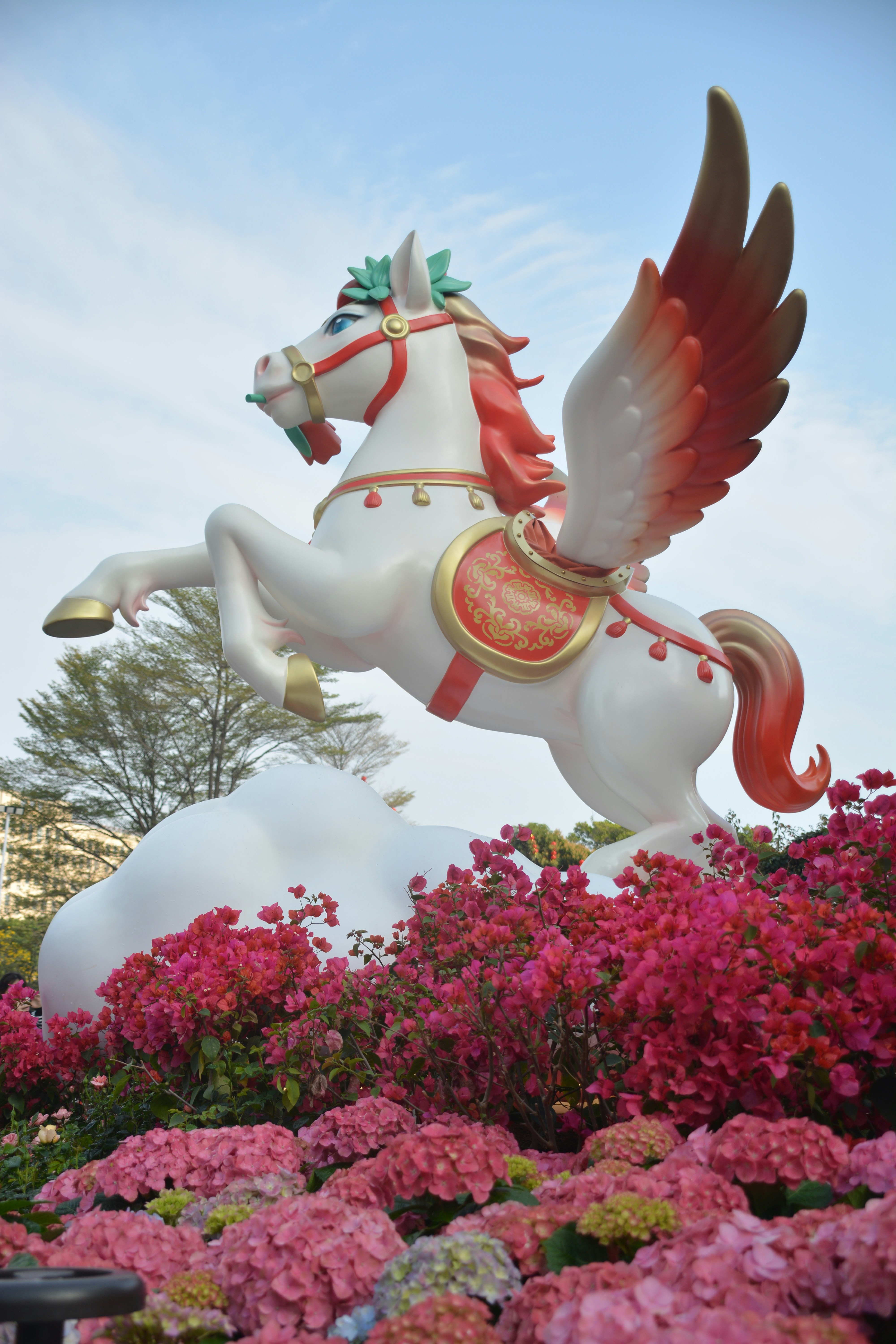 White Pegasus statue rearing above lush pink hydrangeas under a blue sky