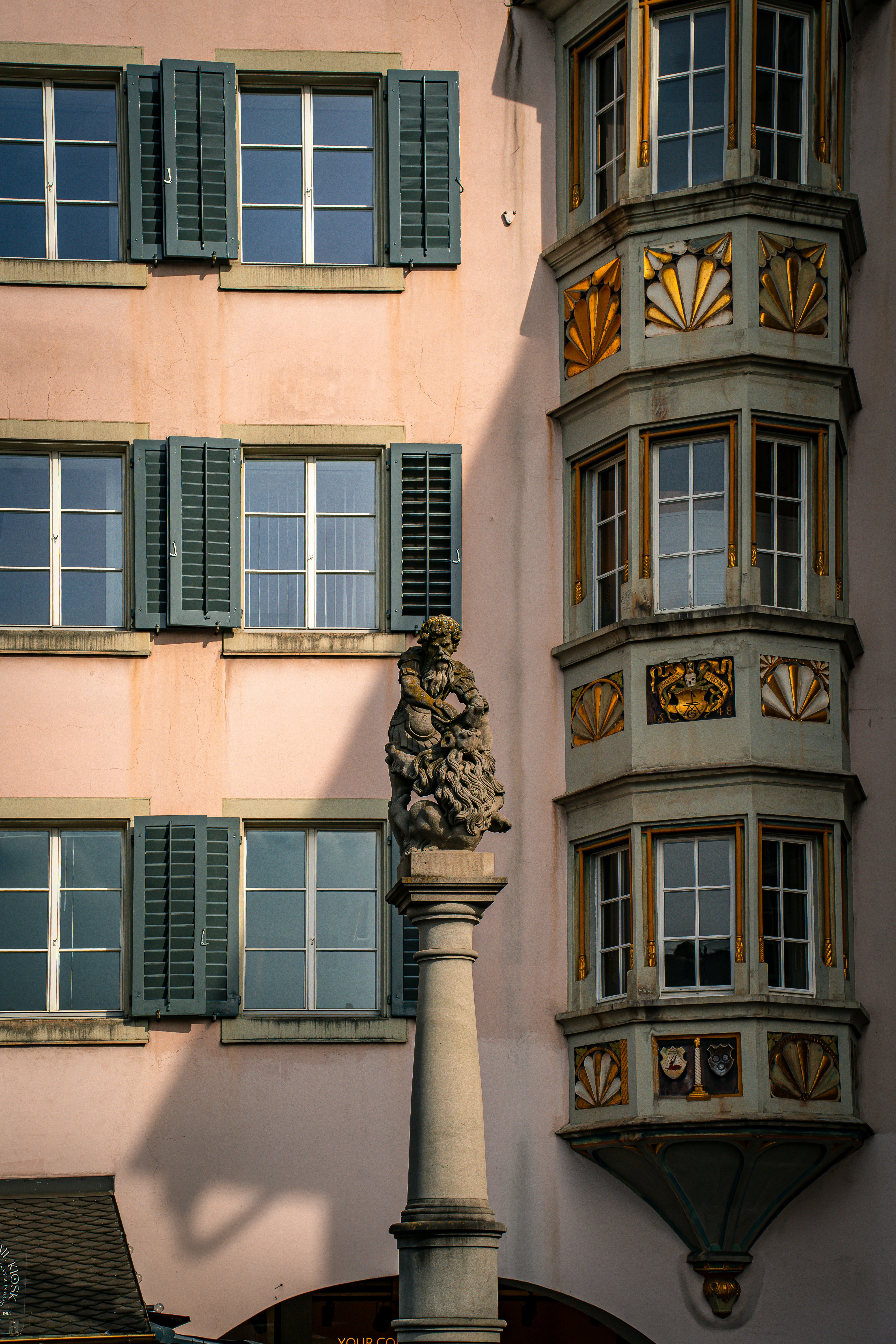 Statue atop a column anchors a pastel facade with ornate bay windows