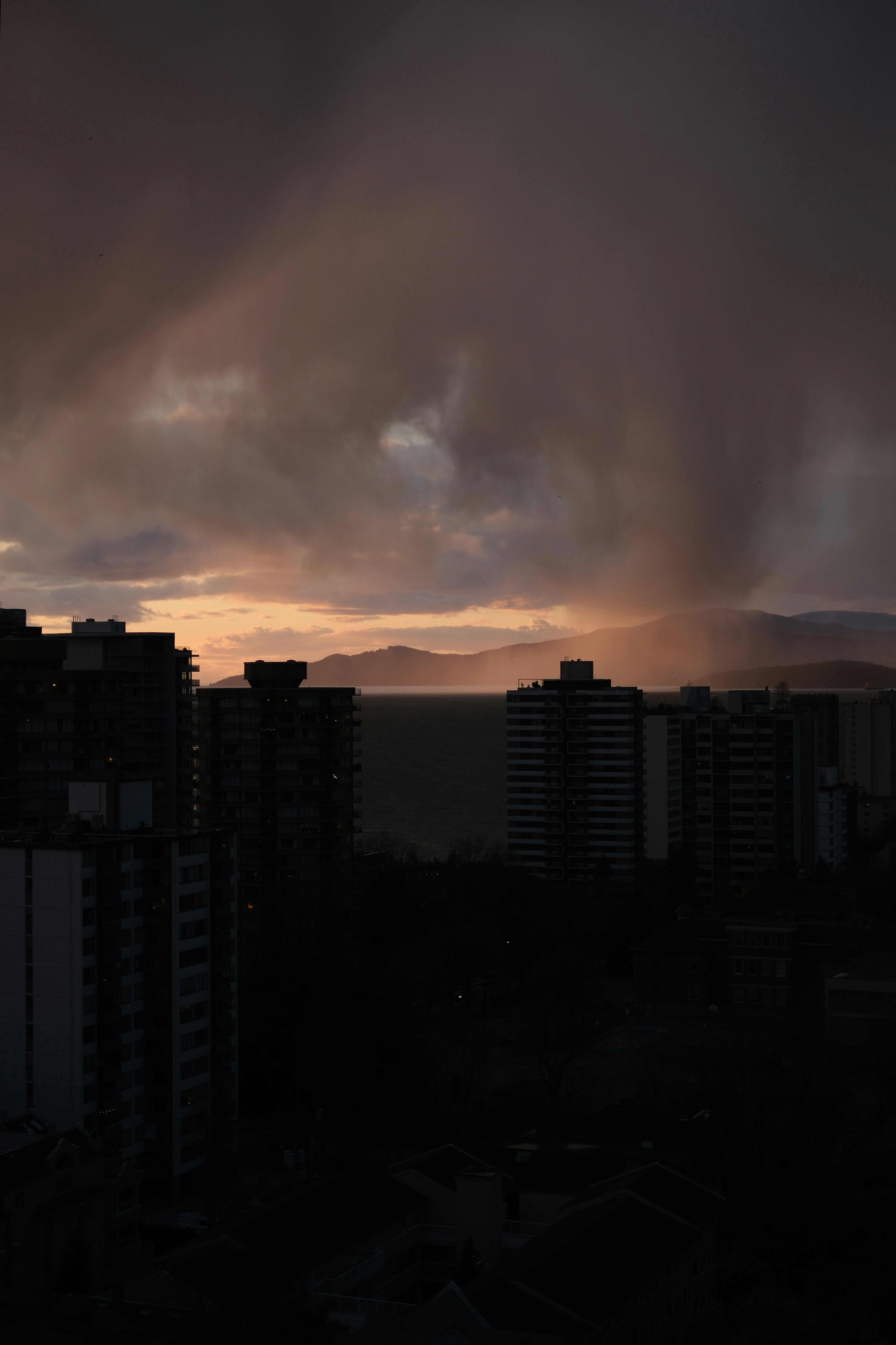 Sunset Currents Over the City: A Rain Veil Meets Distant Peaks