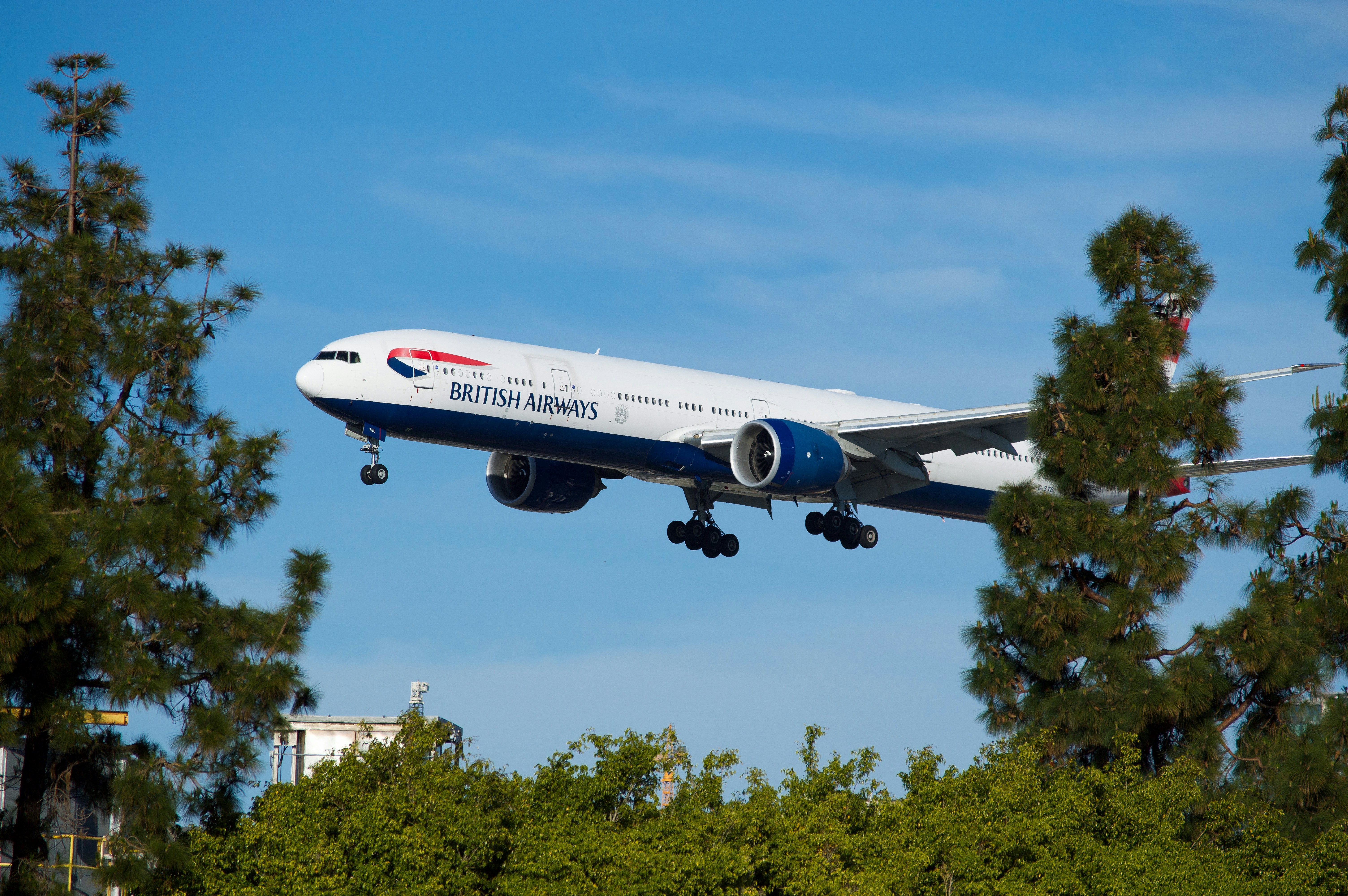 A British Airways jumbo glides toward touchdown above green treetops