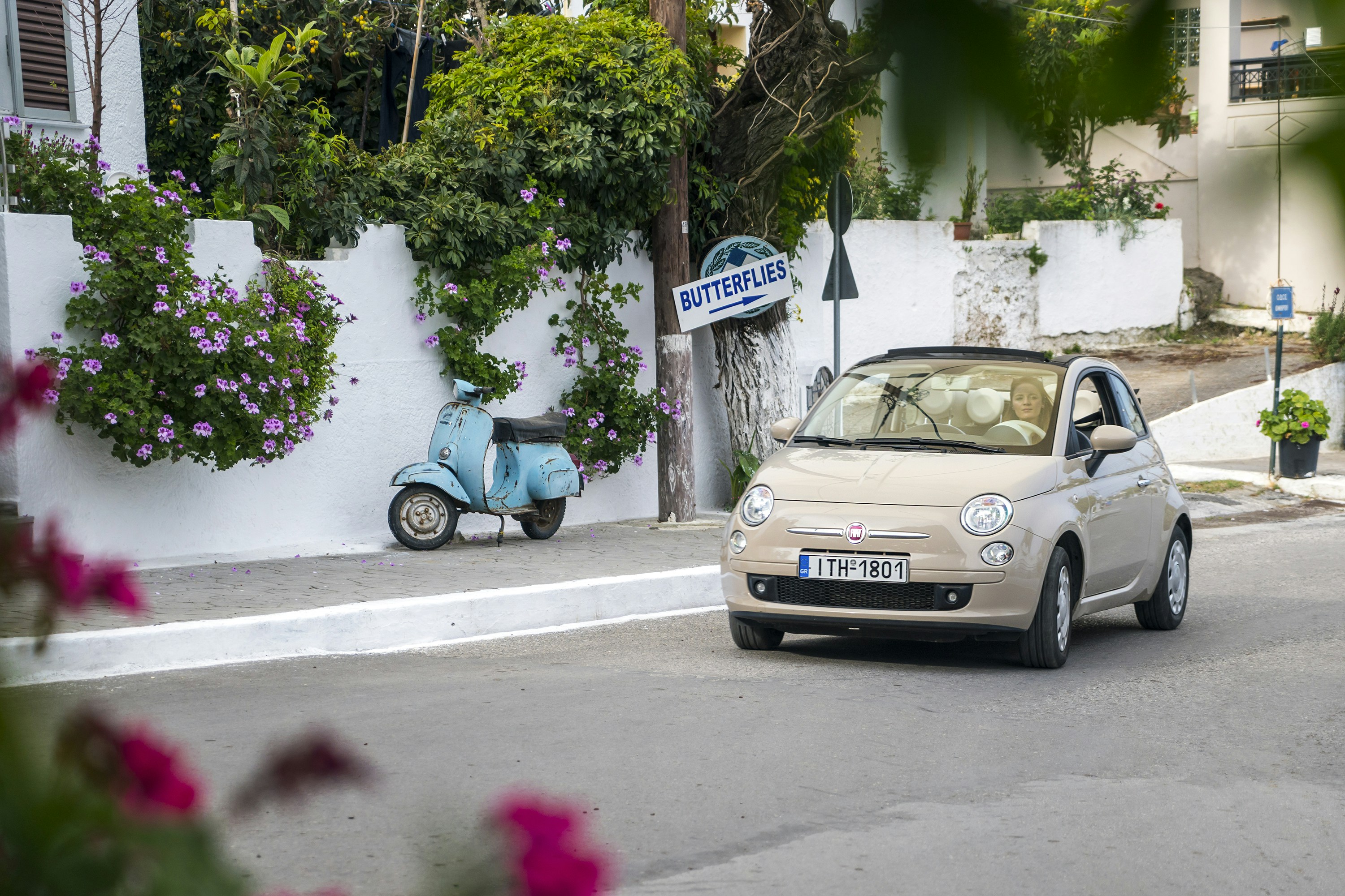 Cream Fiat on a sunlit Mediterranean Street with a Curious Scooter
