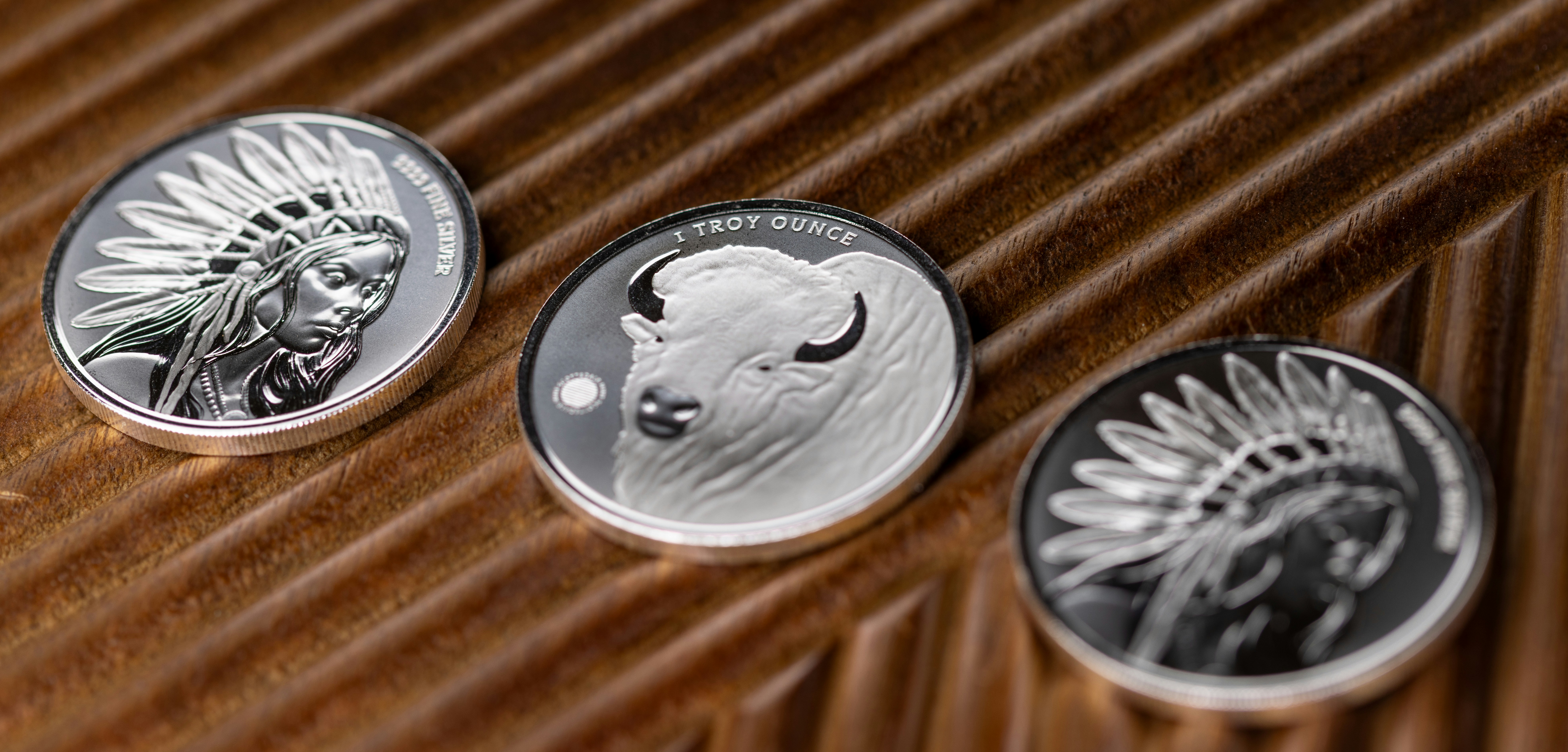 Three collectible coins arranged on a wooden surface, with a Native American chief, bull, and another design visible; a still-life arrangement focusing on metallic texture and engraved details.