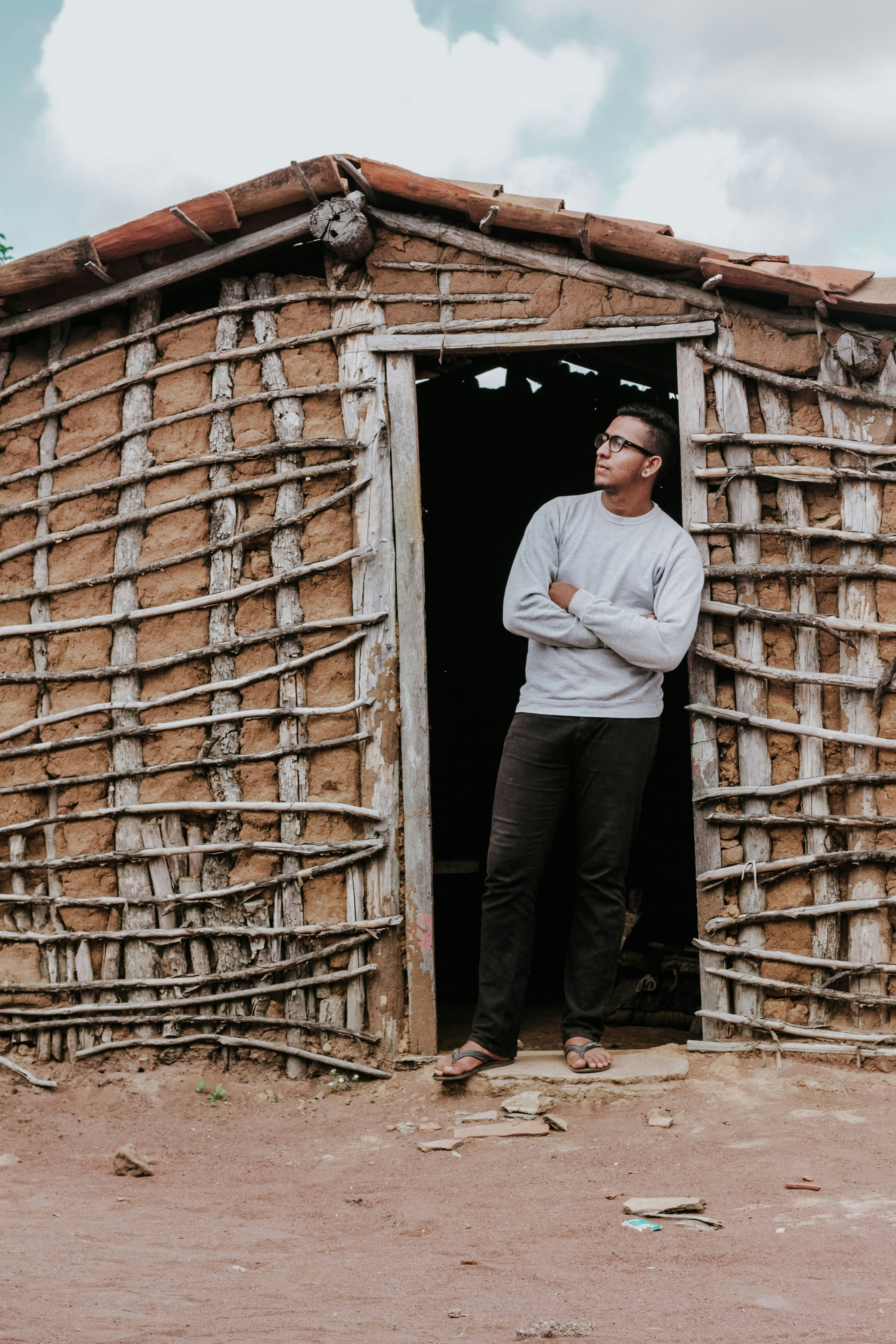 Man in a light sweater standing at the threshold of a handmade hut