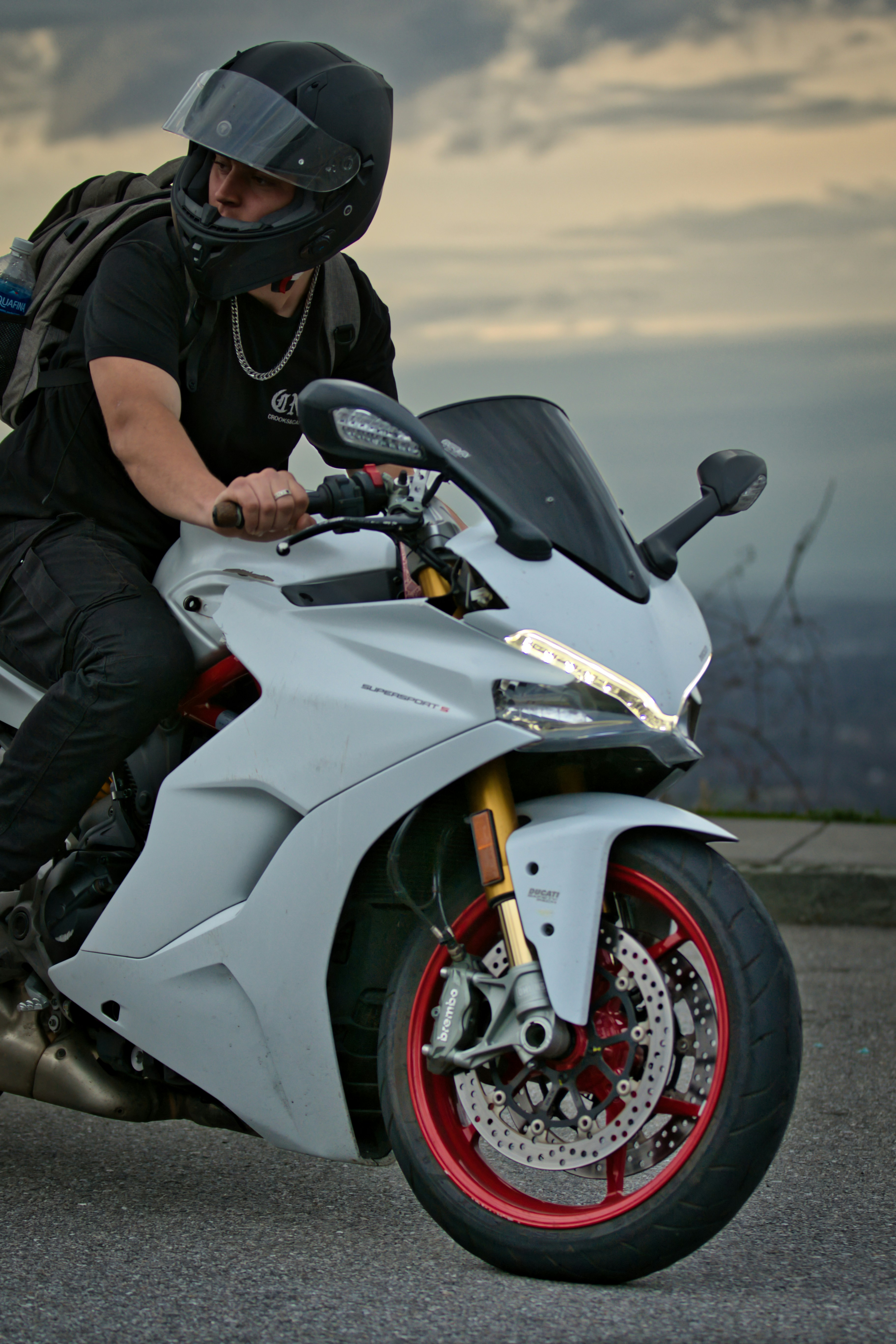 Rider in black on a sleek white sportbike, braced against a windswept horizon
