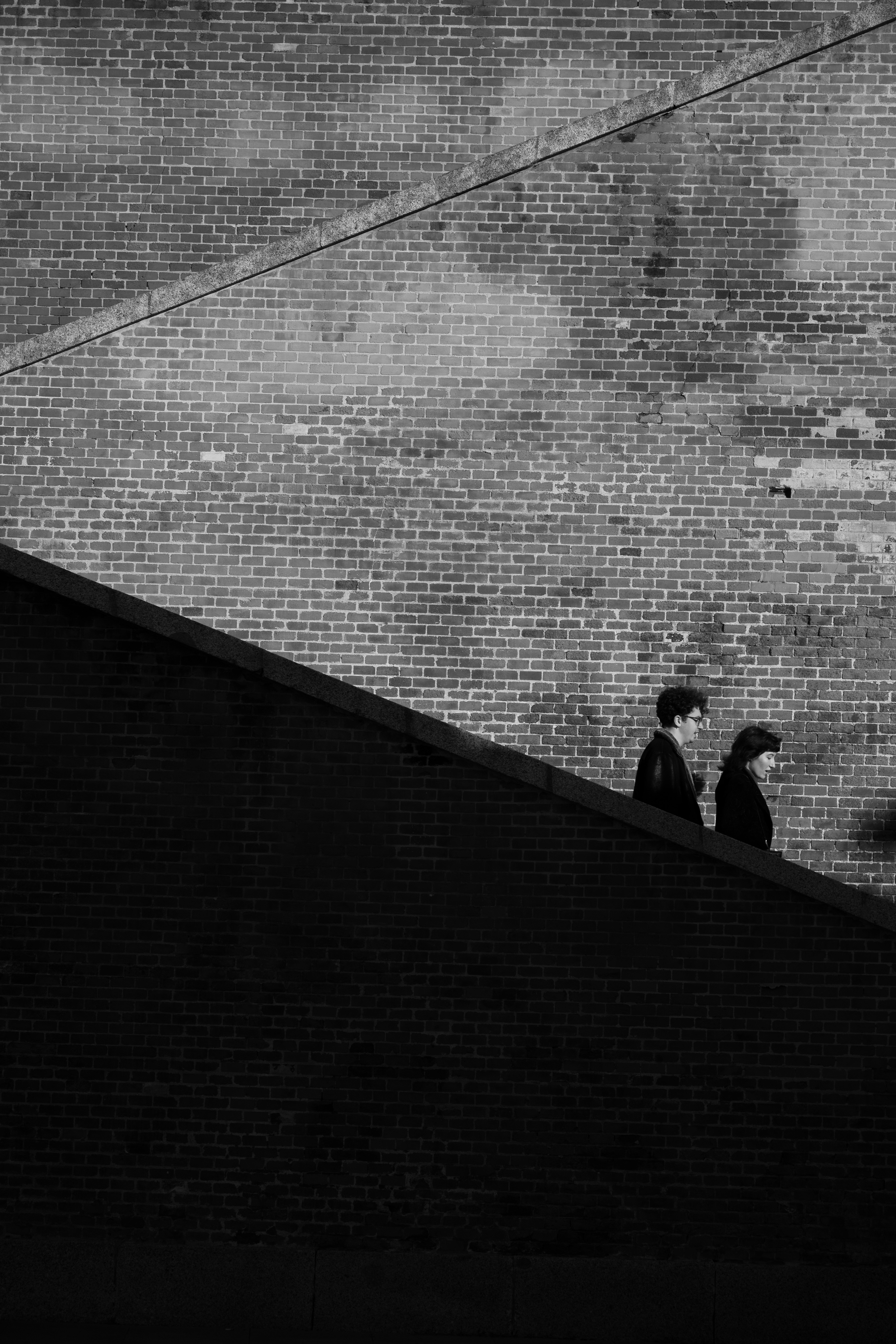 Two Figures Ascend the Bricked Slope under a Diagonal Line