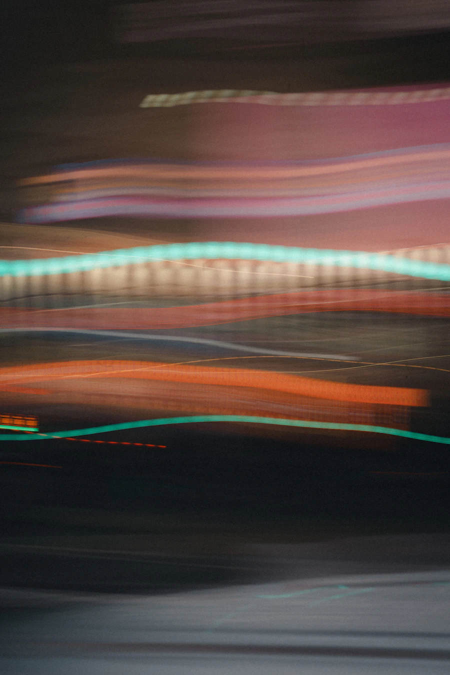 Blurred streaks of city lights swirl across the frame, conveying motion and energy in low light. An abstract urban nightscape emphasizes color and rhythm over detail.