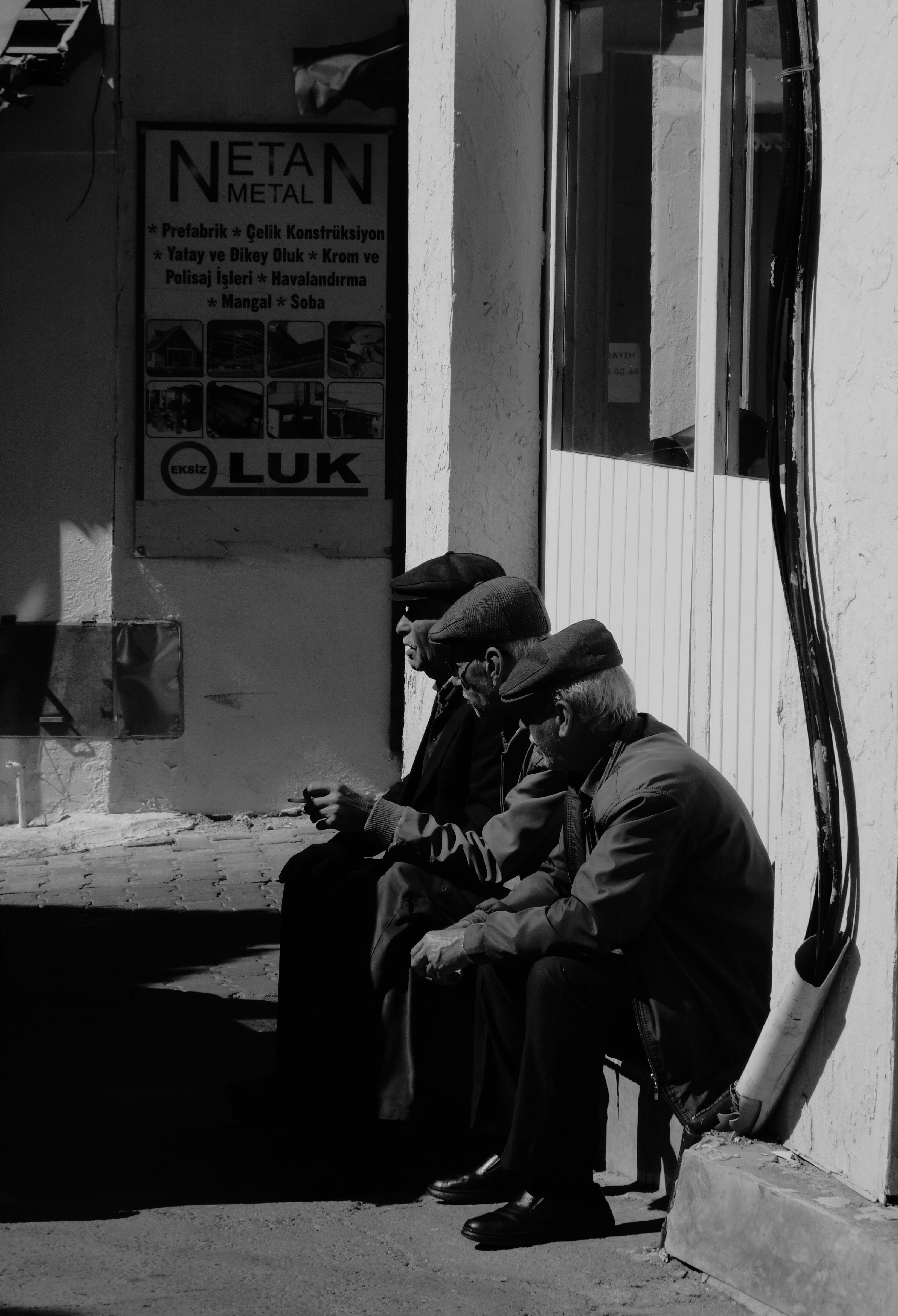 Three Elderly Men on a Sunlit Curb, Shadows Casting a Quiet Dialogue