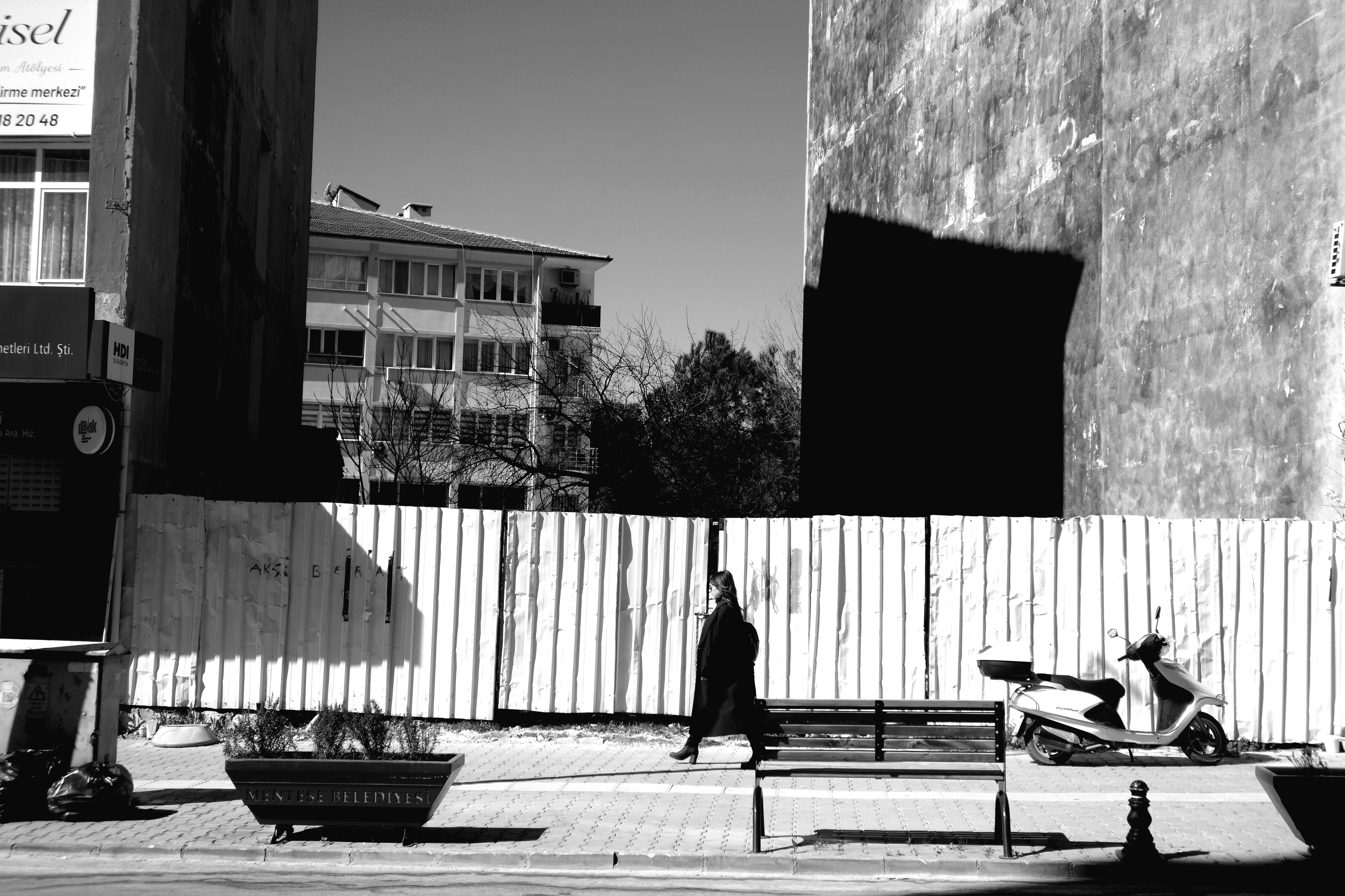 Urban Boundary: Pedestrian and Scooter in a Quiet Fence Day