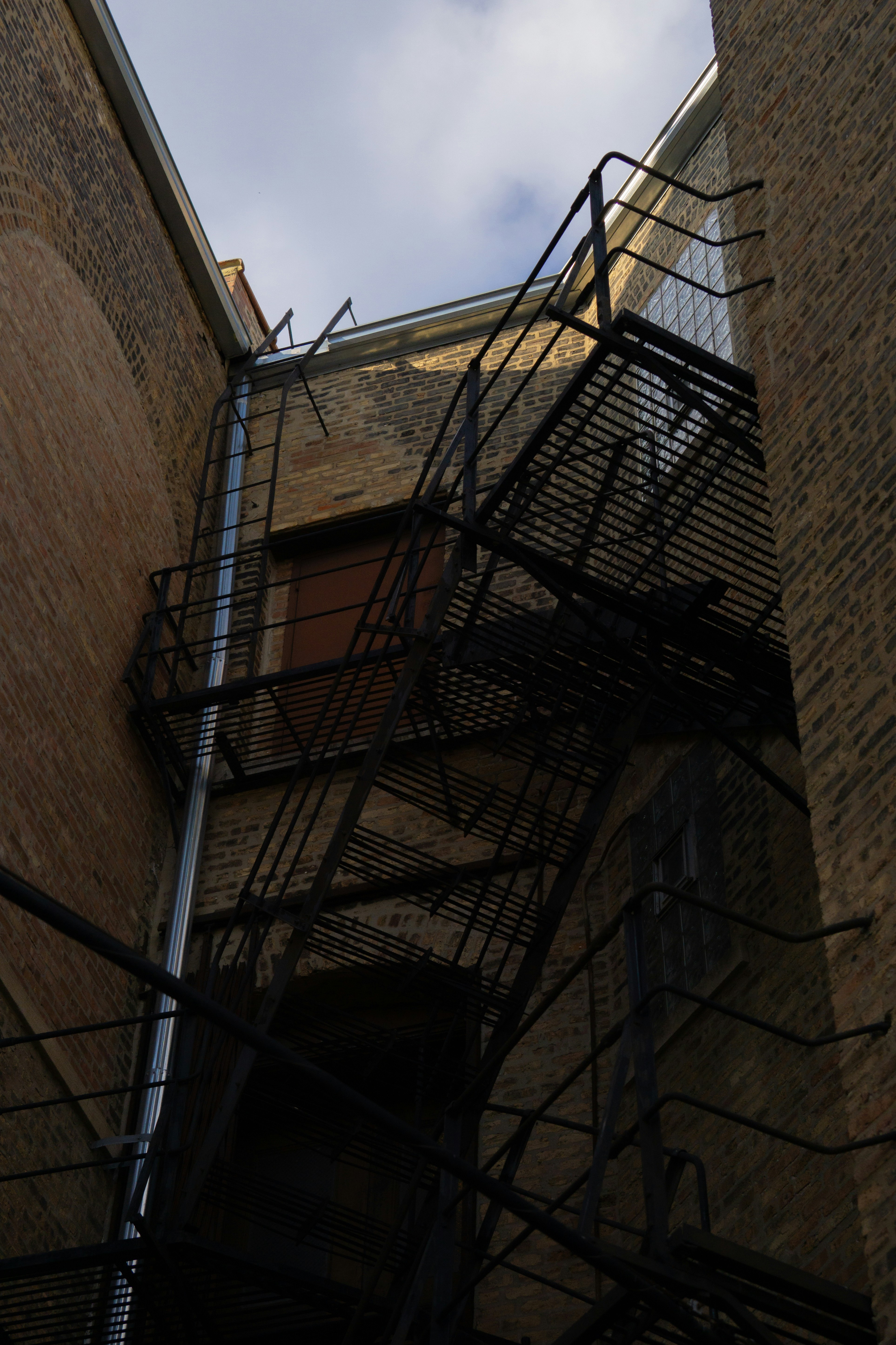 Urban Skyward: Fire Escape Web Over a Narrow Brick Shaft