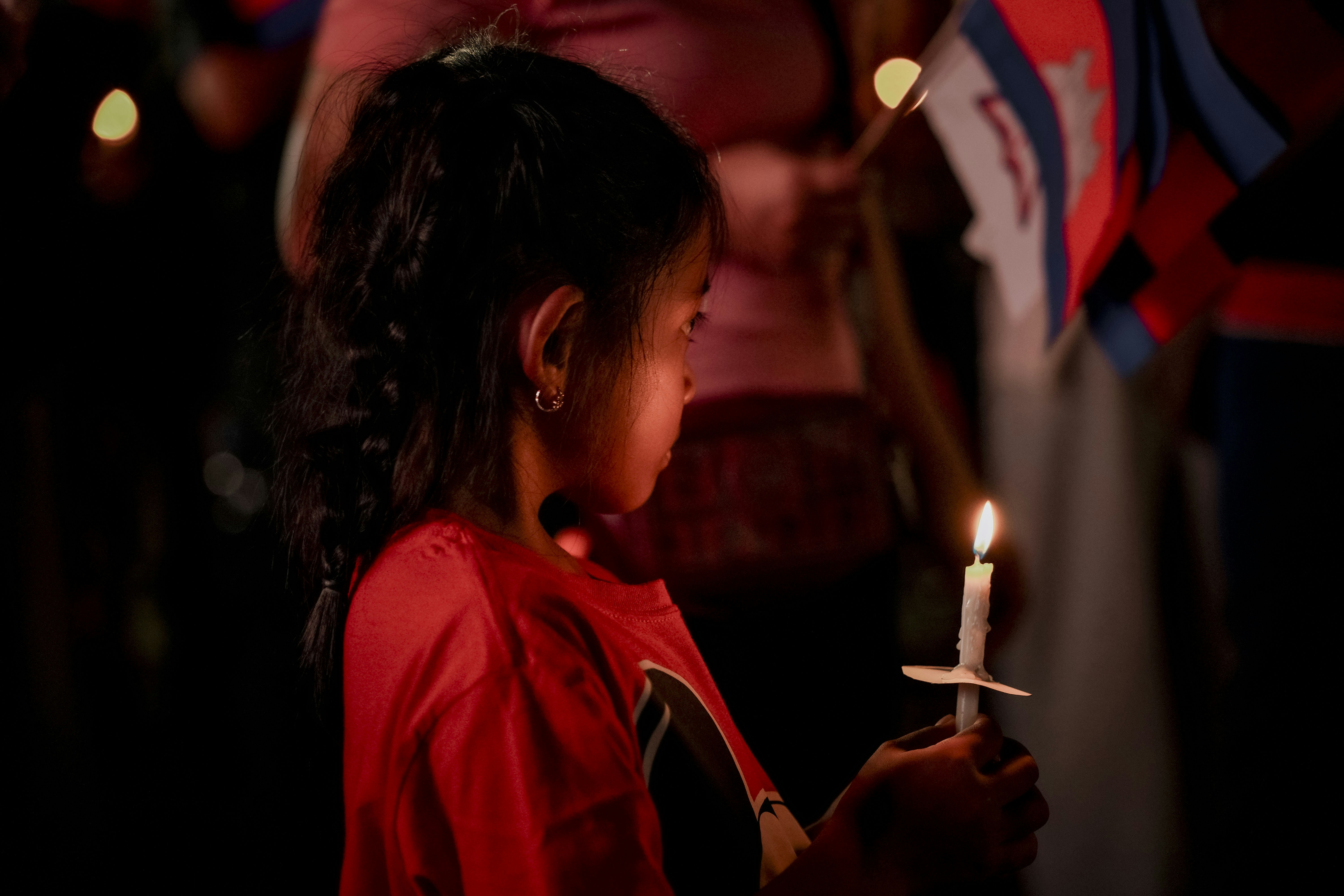 Candlelit Vigil: A Young Girl in Red at Night