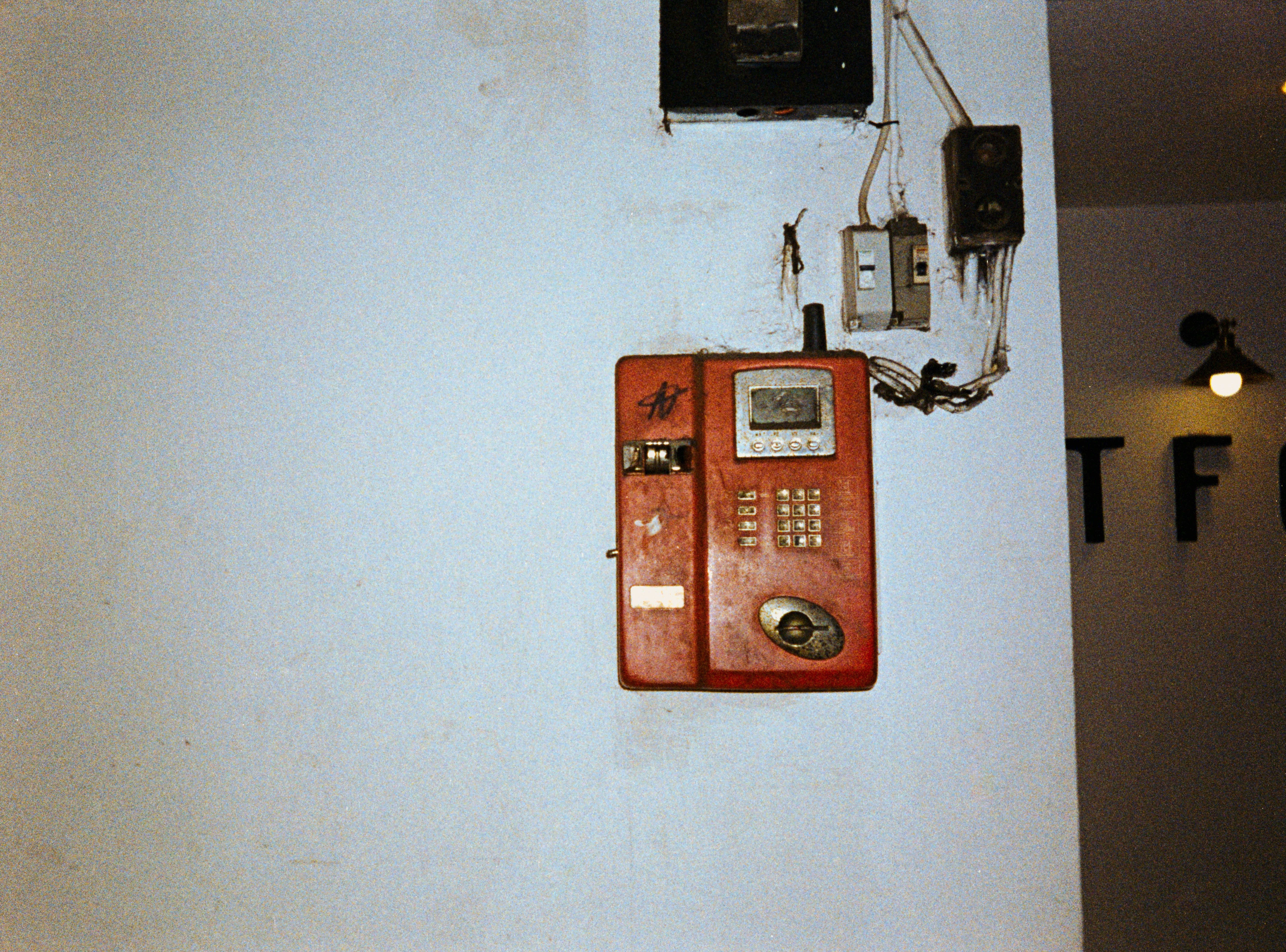 A vintage red payphone mounted on a light blue wall.