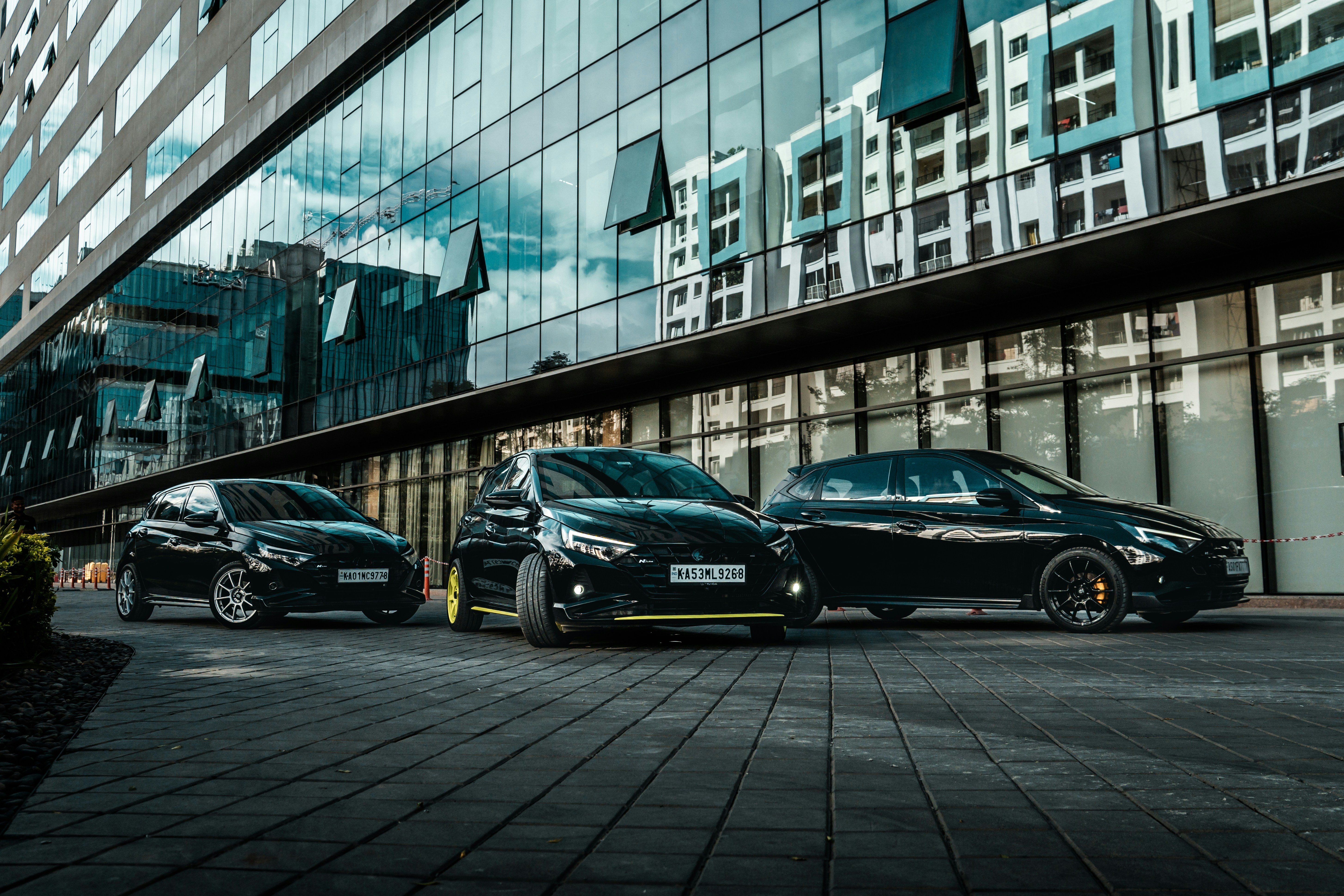 Three Dark Cars Resting Along a Modern Glass Facade