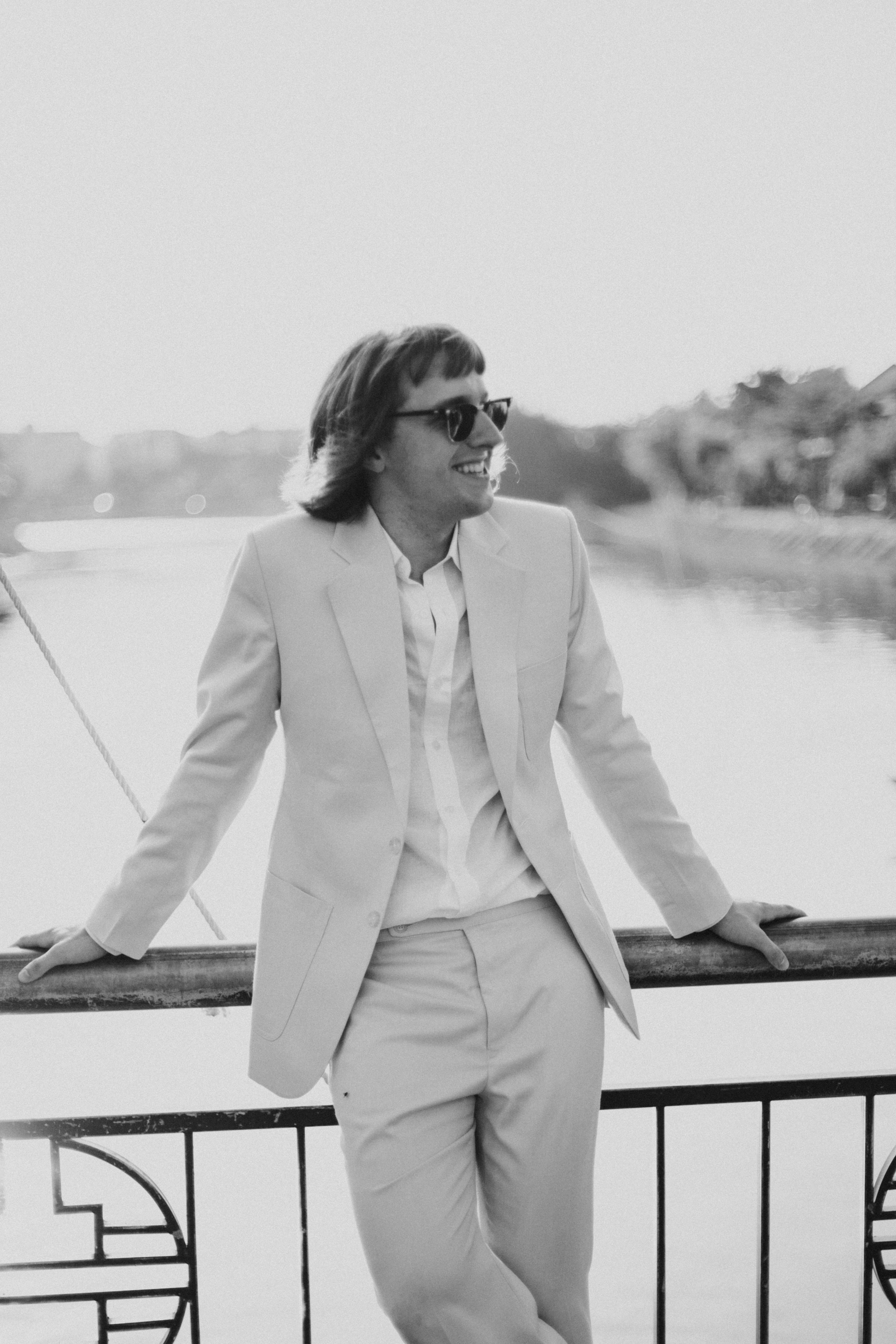 Smiling figure in light suit leaning on railing by waterfront