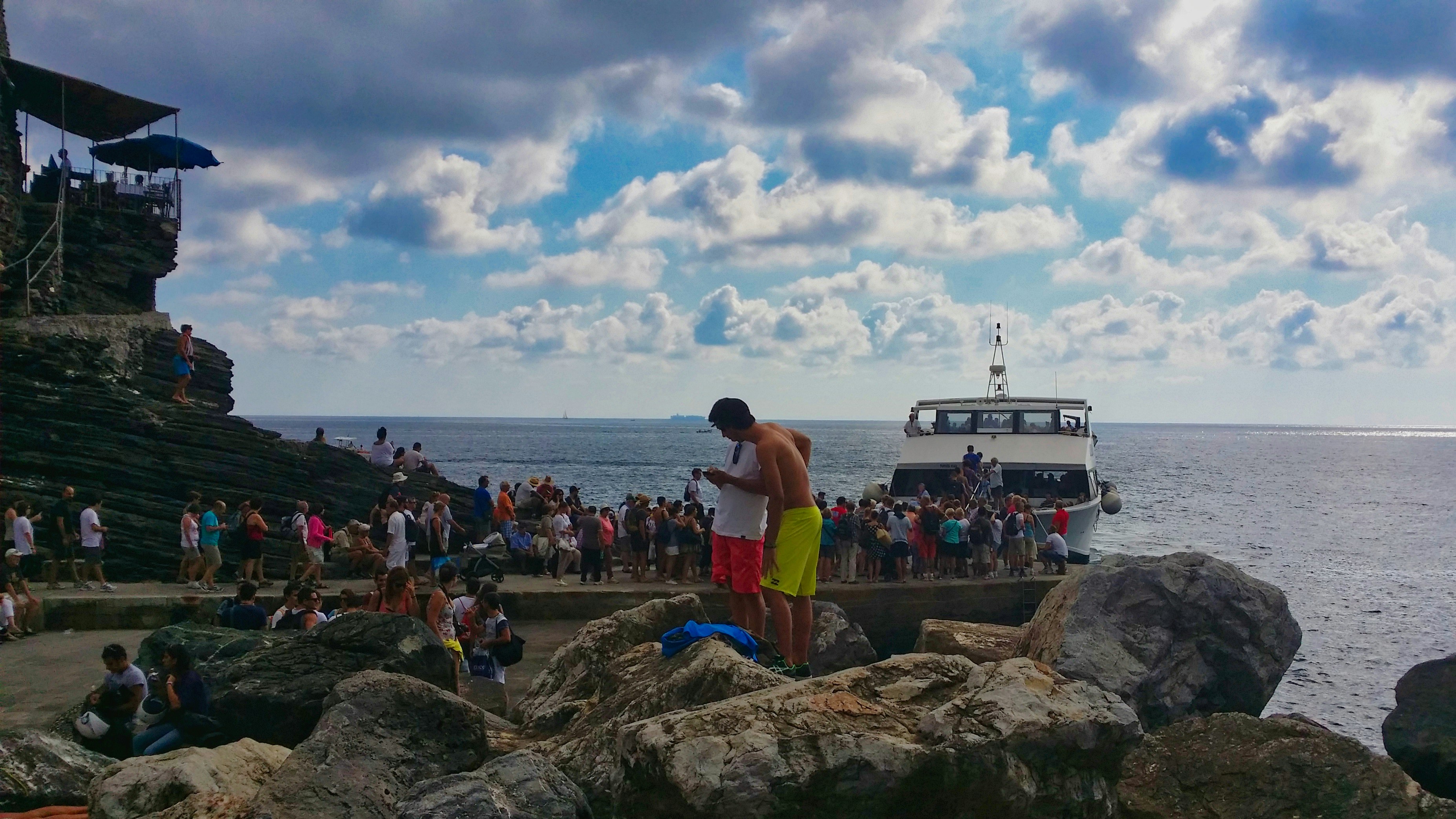 People gathered by the water with a boat nearby.