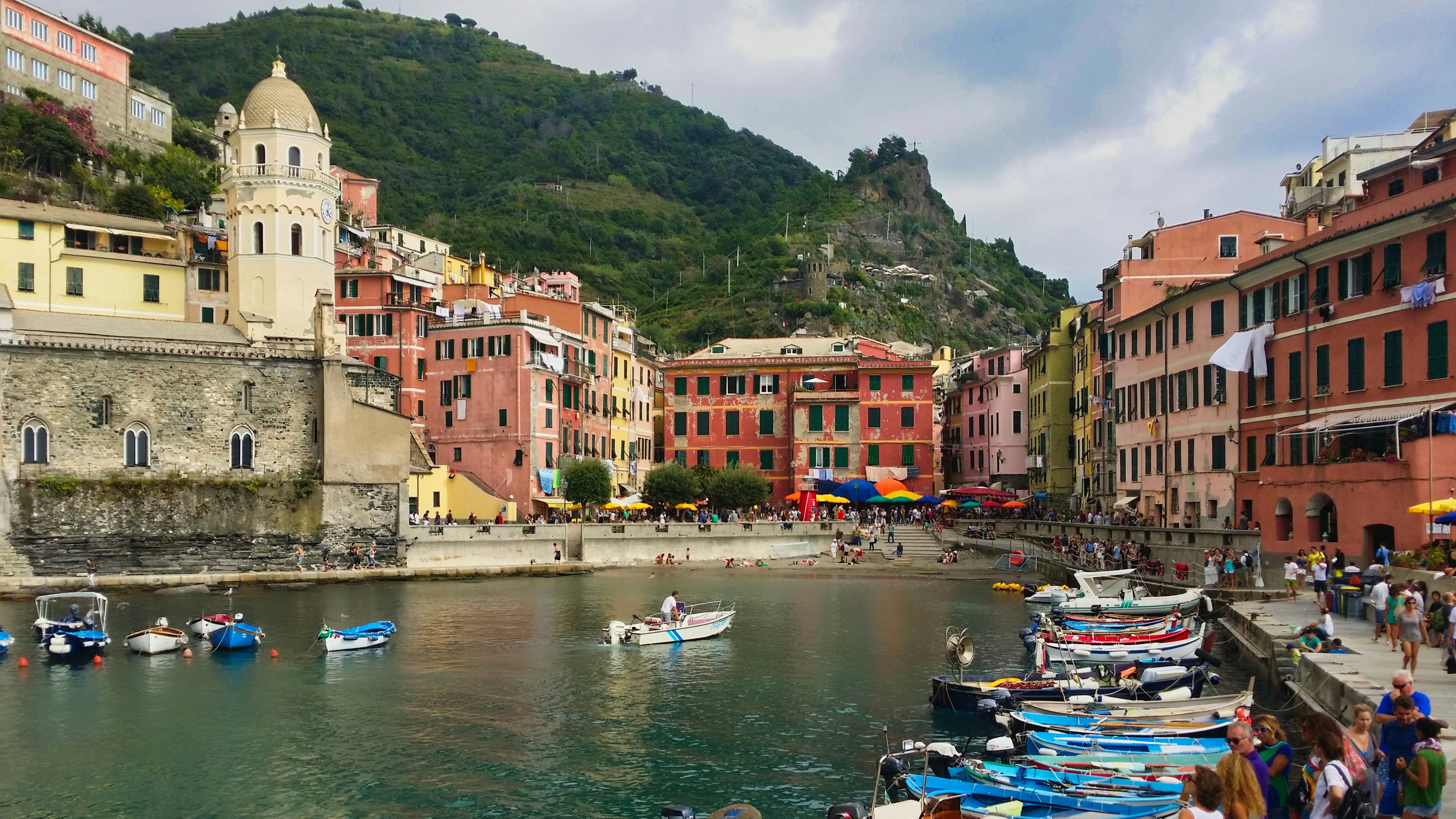Colorful buildings line a harbor with boats and mountains.