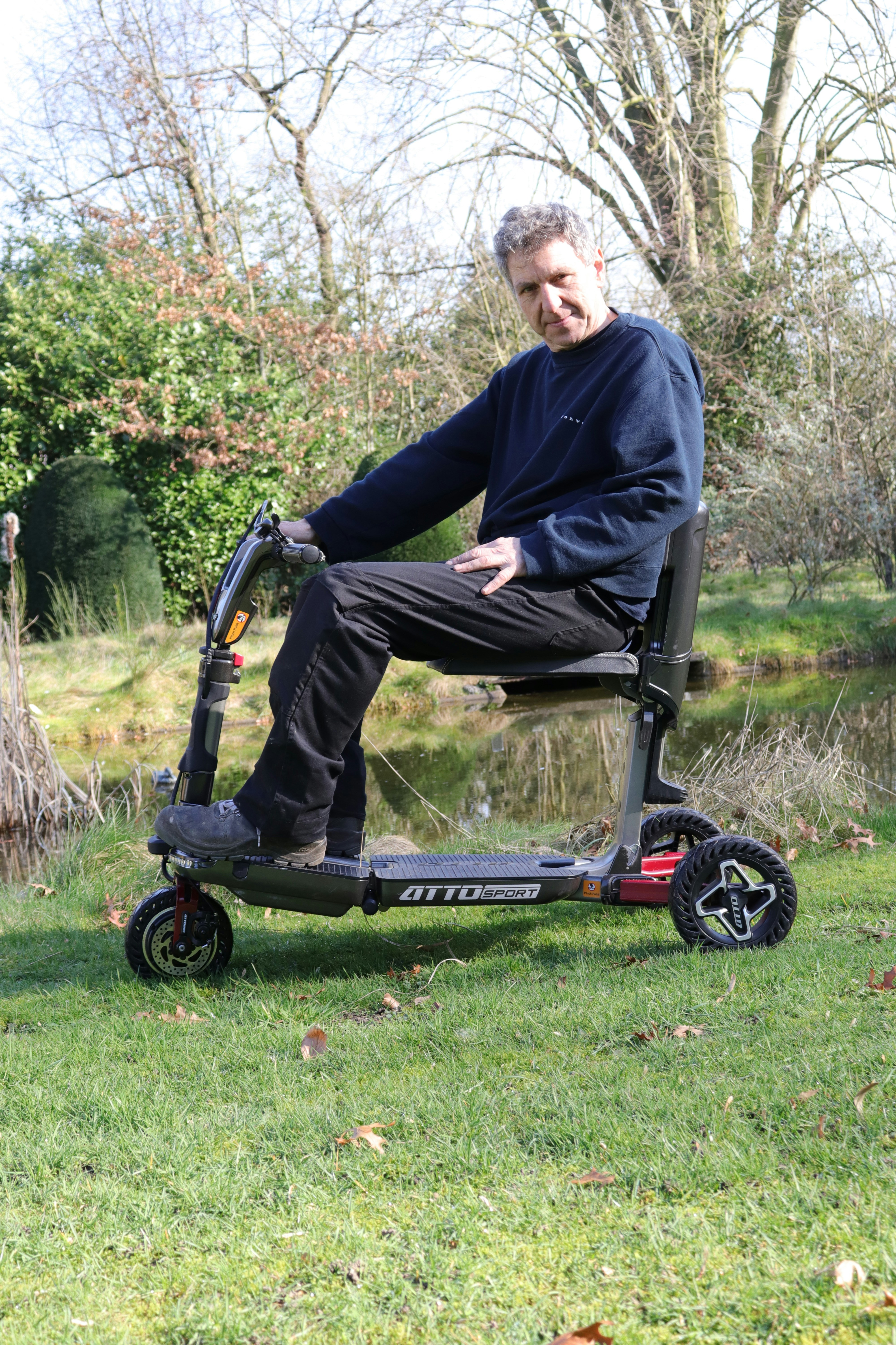 Man on a mobility scooter pauses by the pond on a sunny day