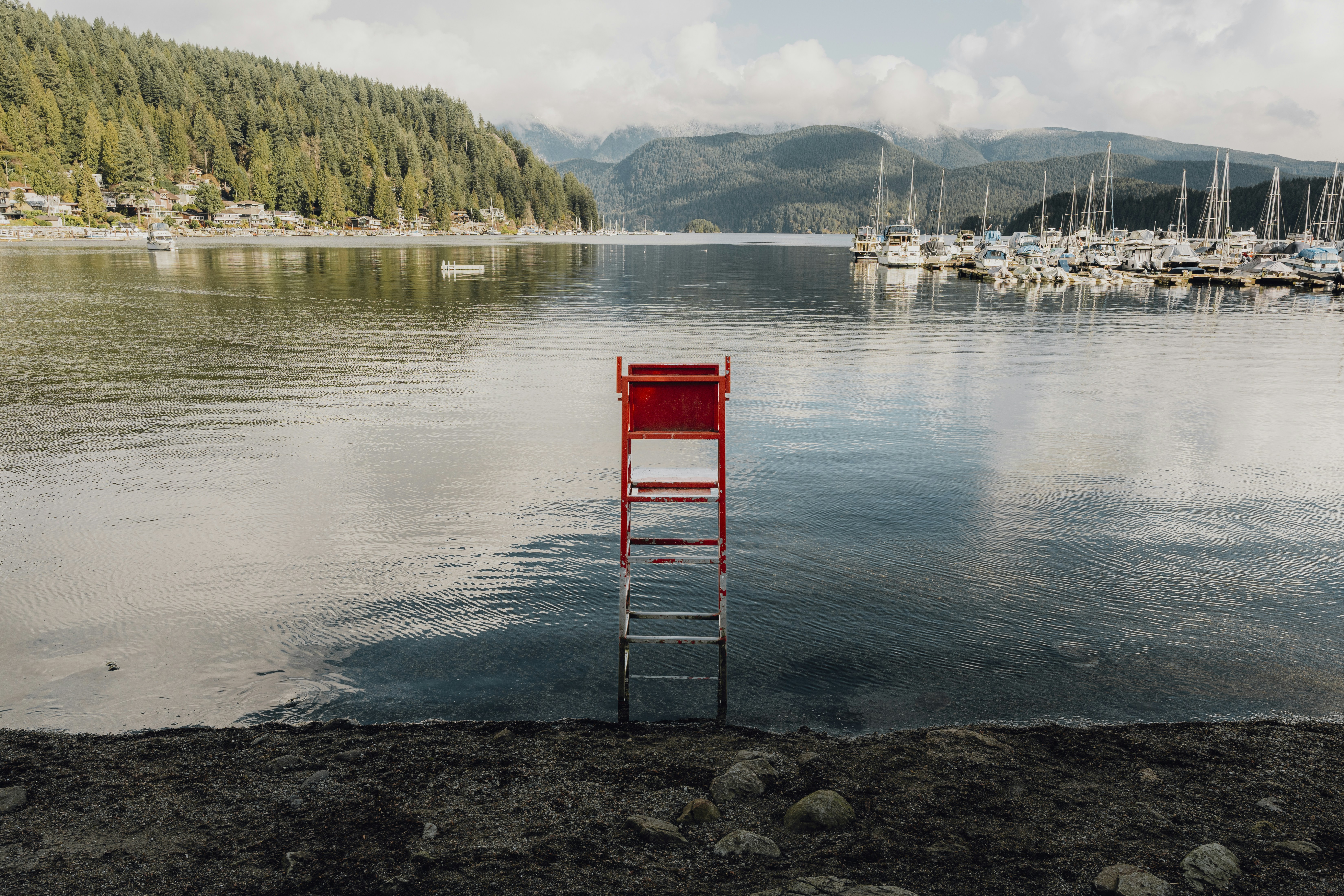 Red Lifeline Over Calm Waters: A Lone Rescue Chair Against a Mountain Harbor