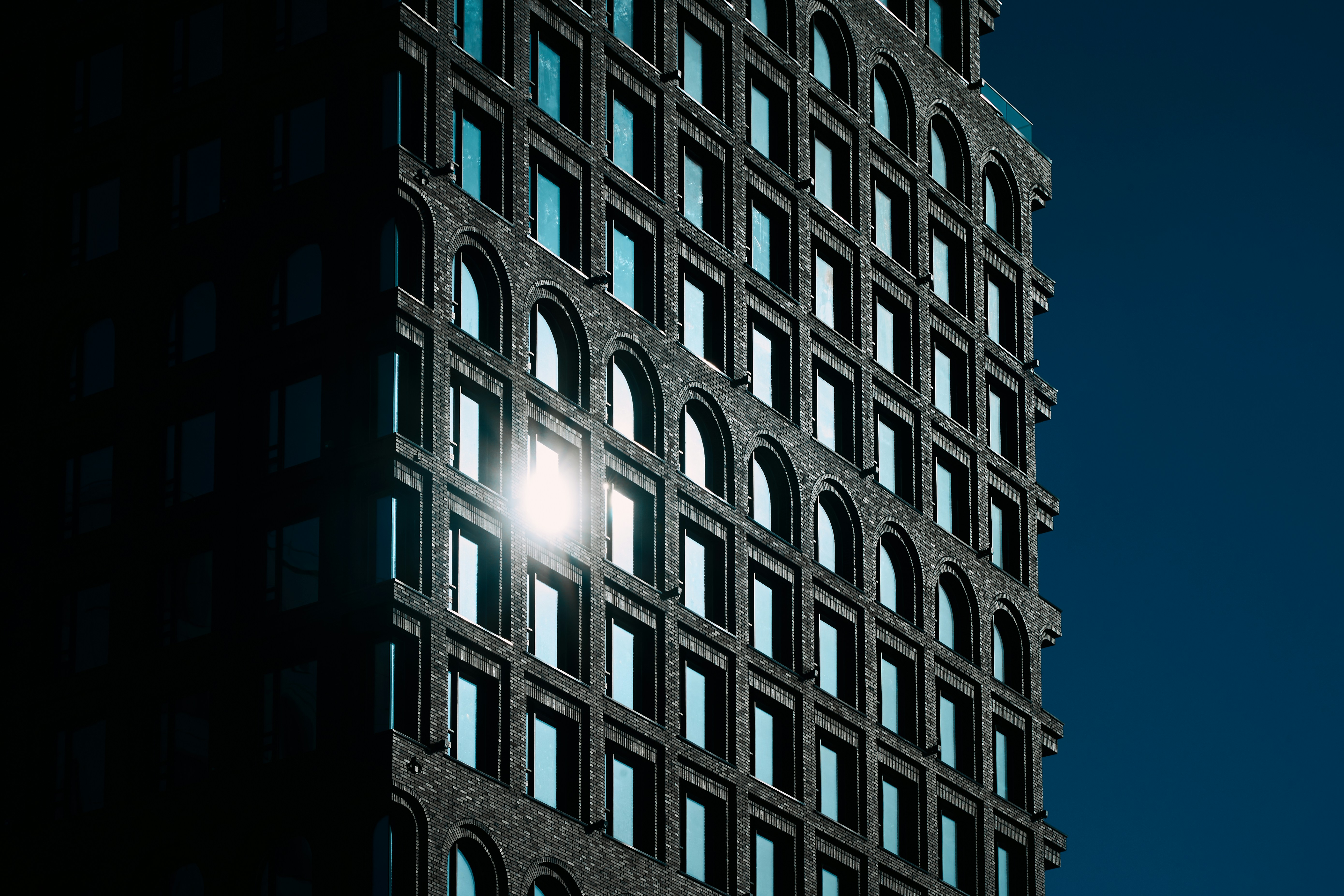 Sunlit Facade: Arched Windows and Gleaming Patch on a Brick Tower